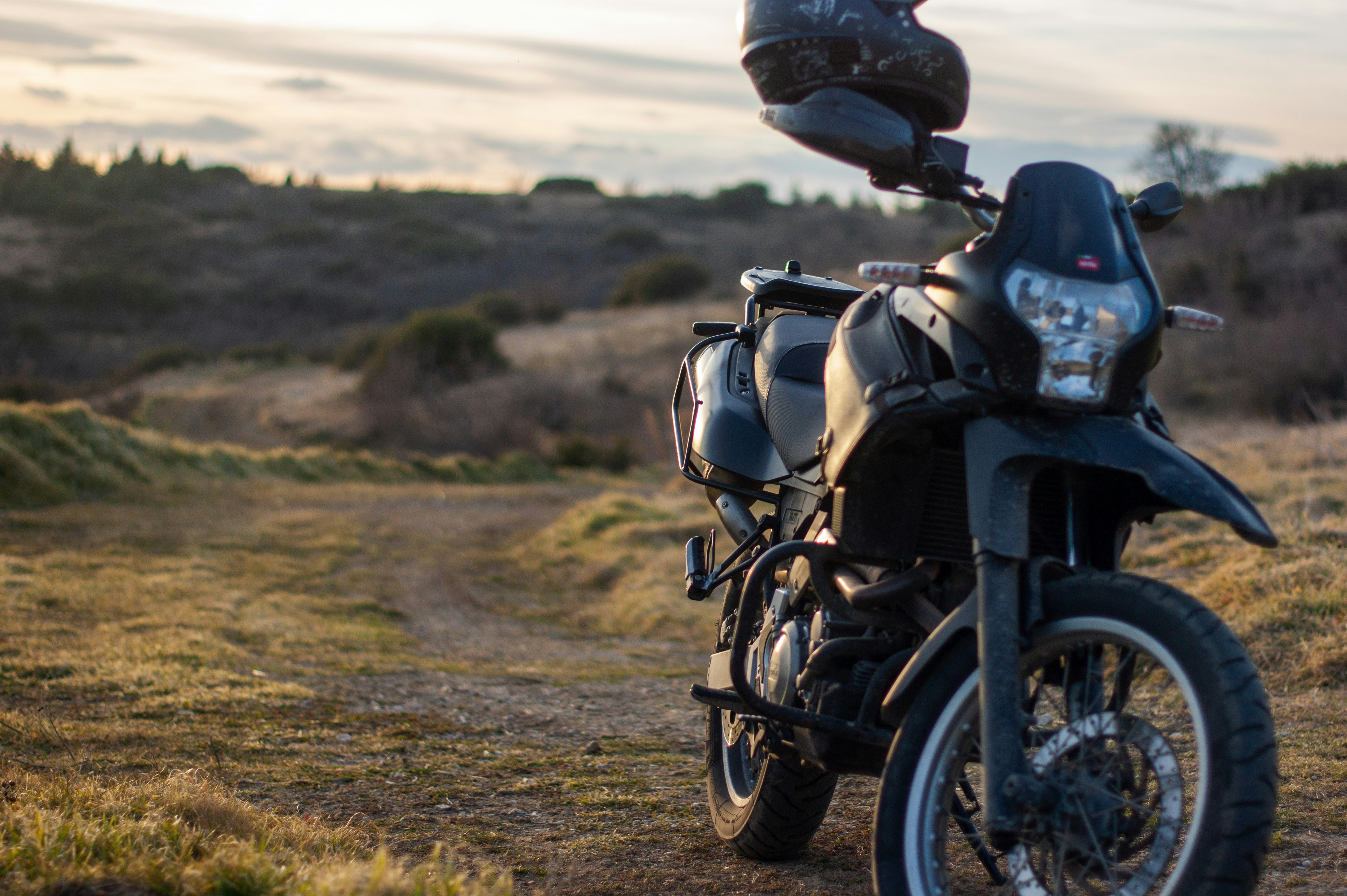 Black motorcycle parked on a sunlit dirt trail with a scenic countryside backdrop.