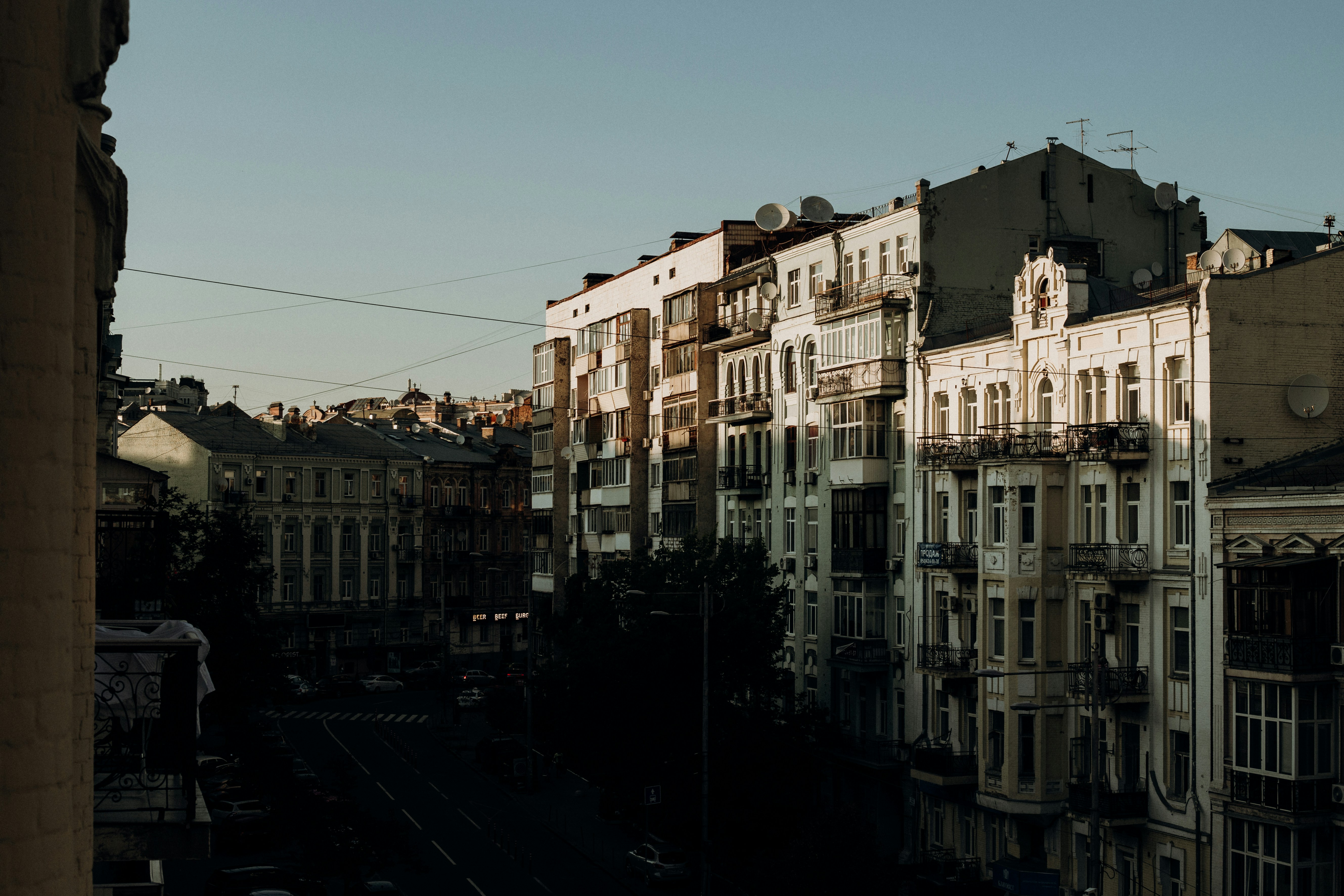 Sunlight casts long shadows on a row of historic buildings lining a quiet street.
