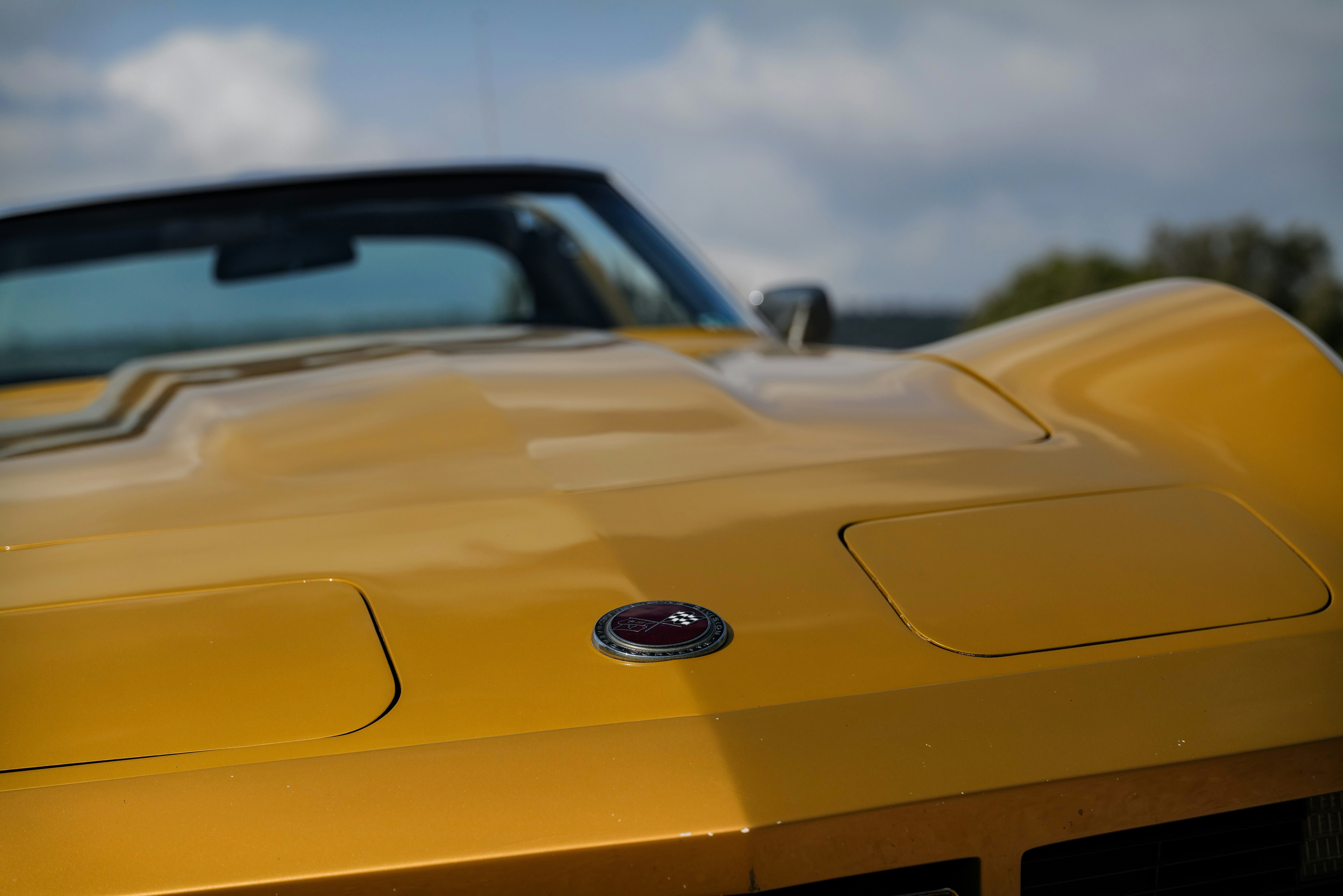 Close-up of a vintage yellow car hood showcasing its sleek lines and emblem. The image captures the essence of automotive craftsmanship.
