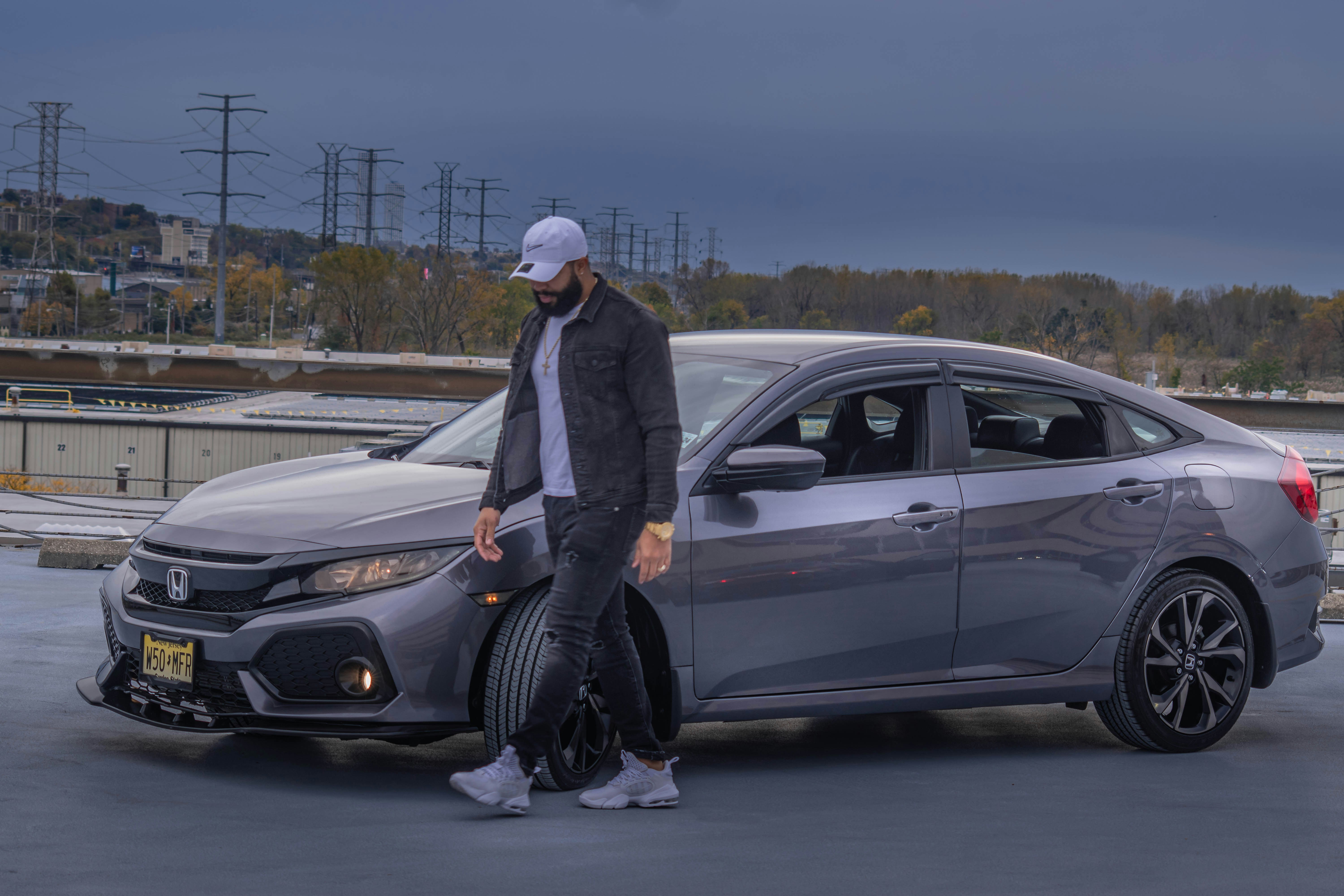 Person standing beside a sleek gray sedan under a cloudy evening sky.