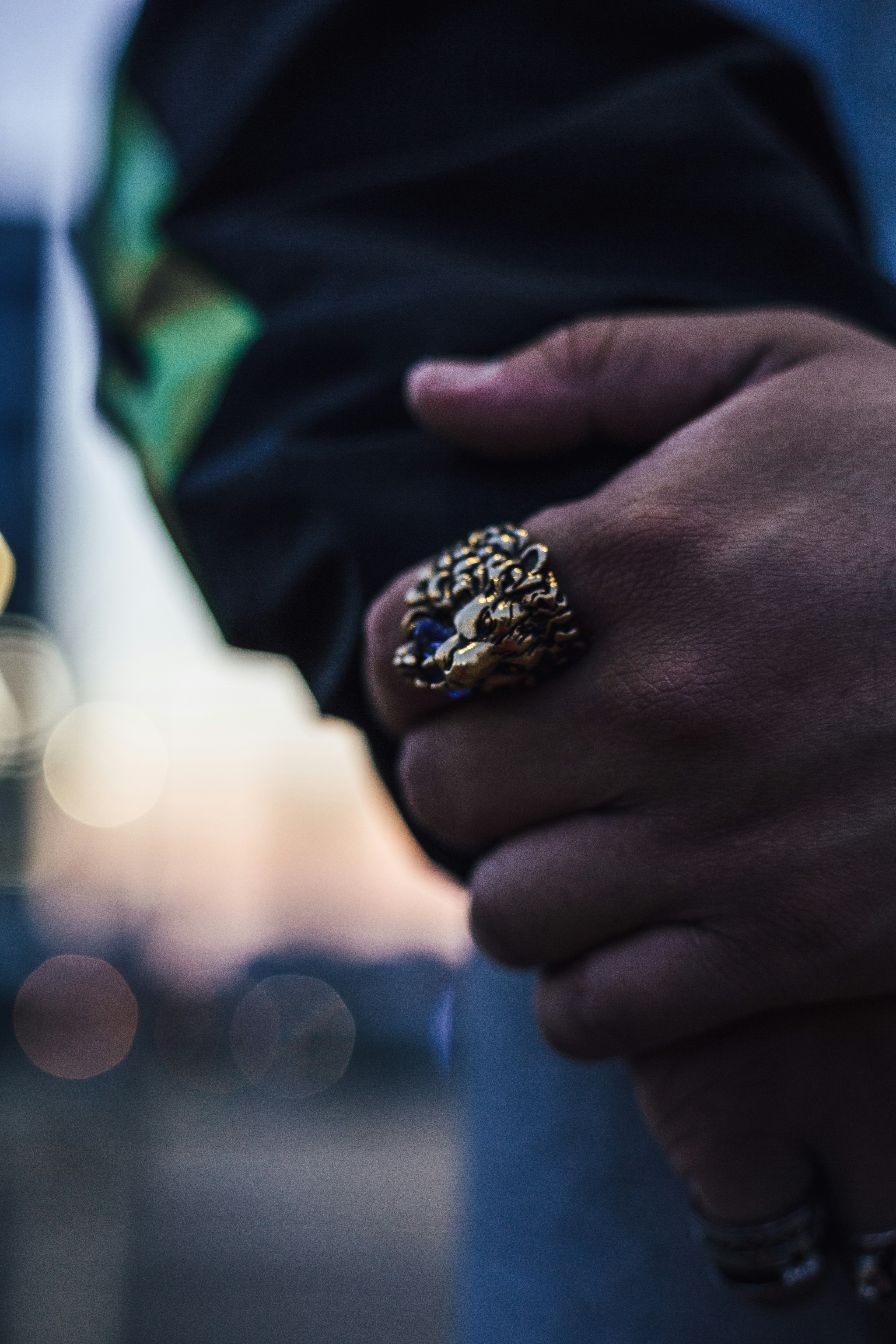 Close-up of a hand adorned with an ornate ring, showcasing intricate details against a softly blurred background of urban twilight.