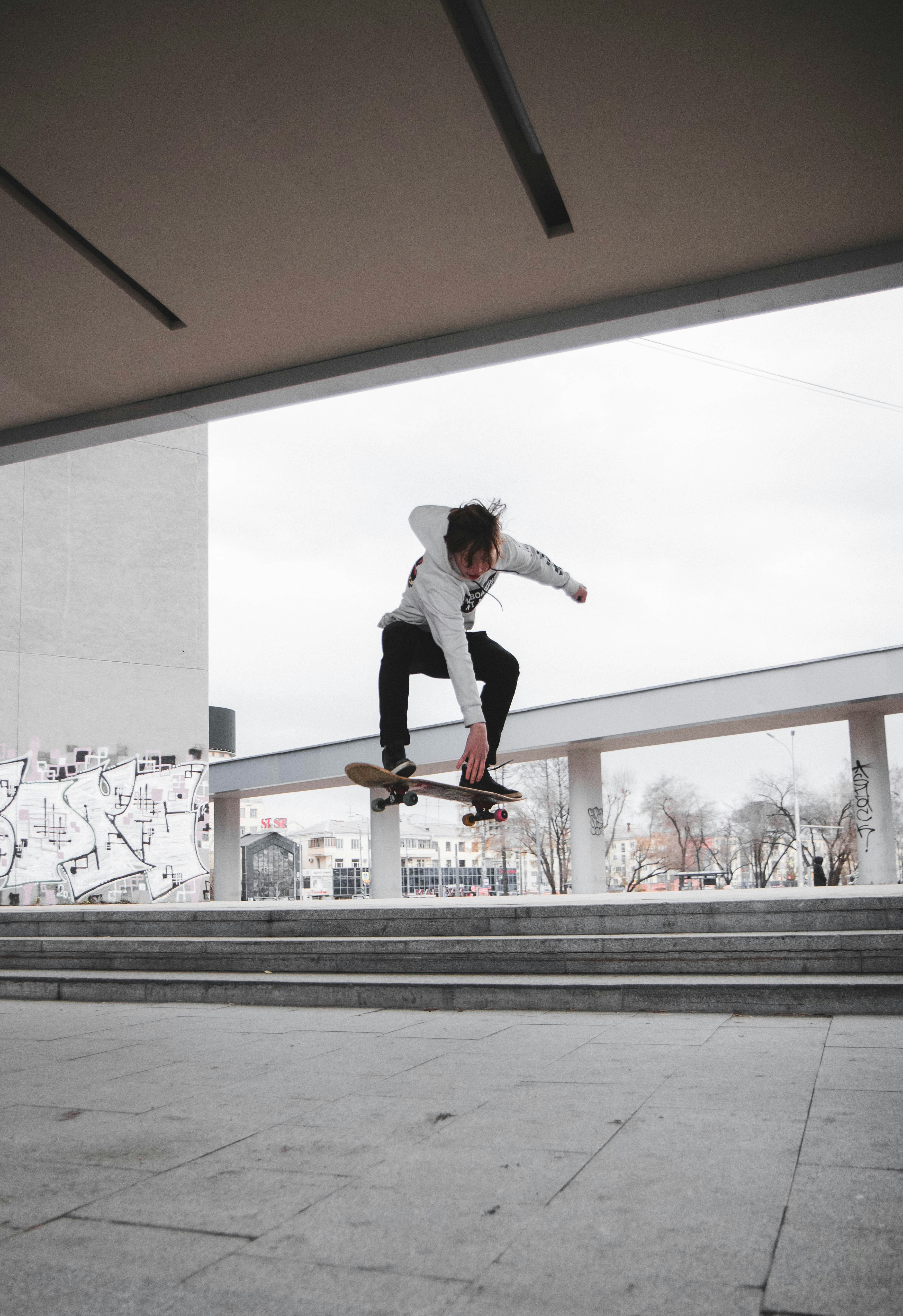 Skateboarder performing a trick mid-air above concrete steps in an urban setting, showcasing dynamic movement and skill.