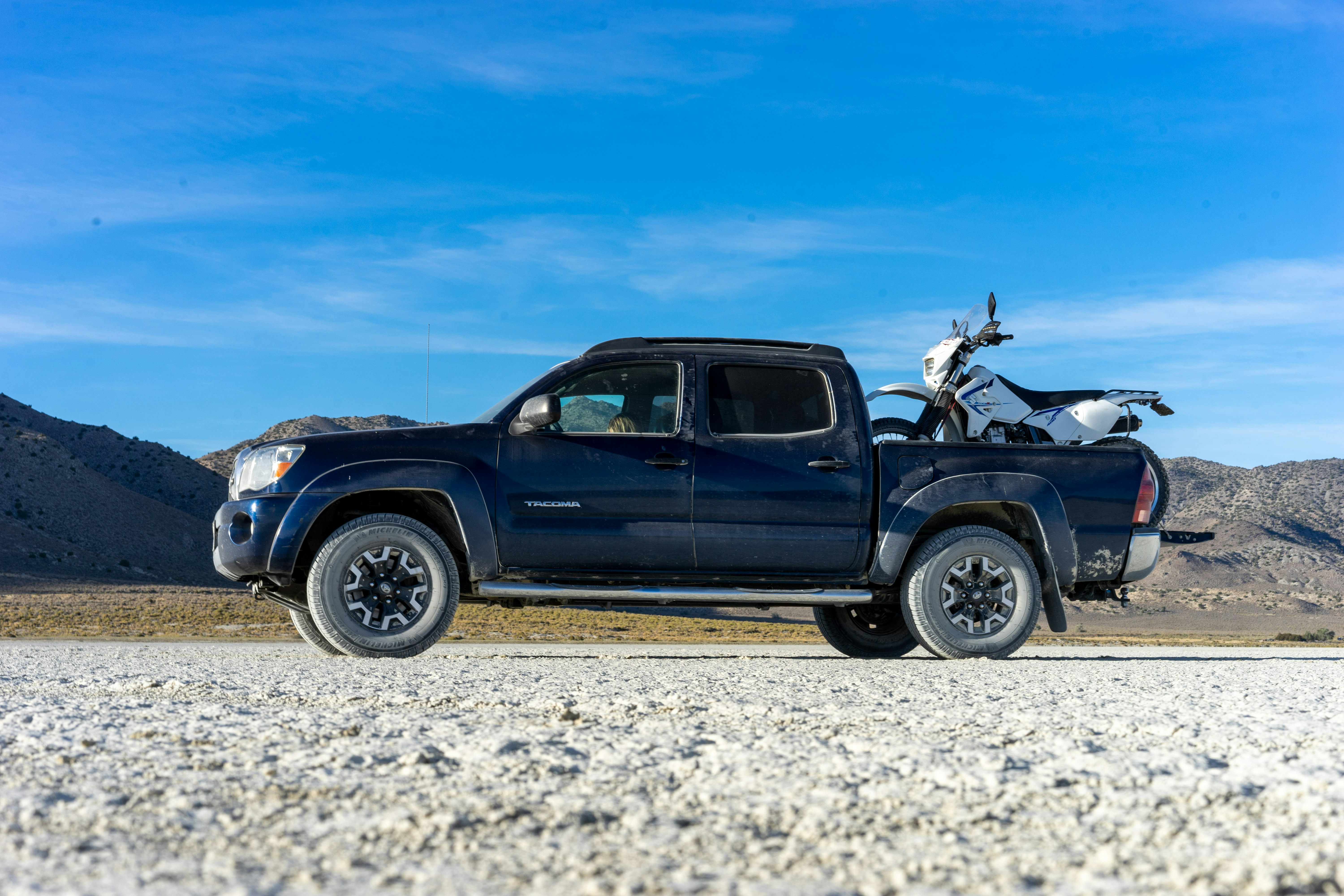 Black pickup truck with a motorcycle in the bed parked on a rocky desert terrain under a clear blue sky.
