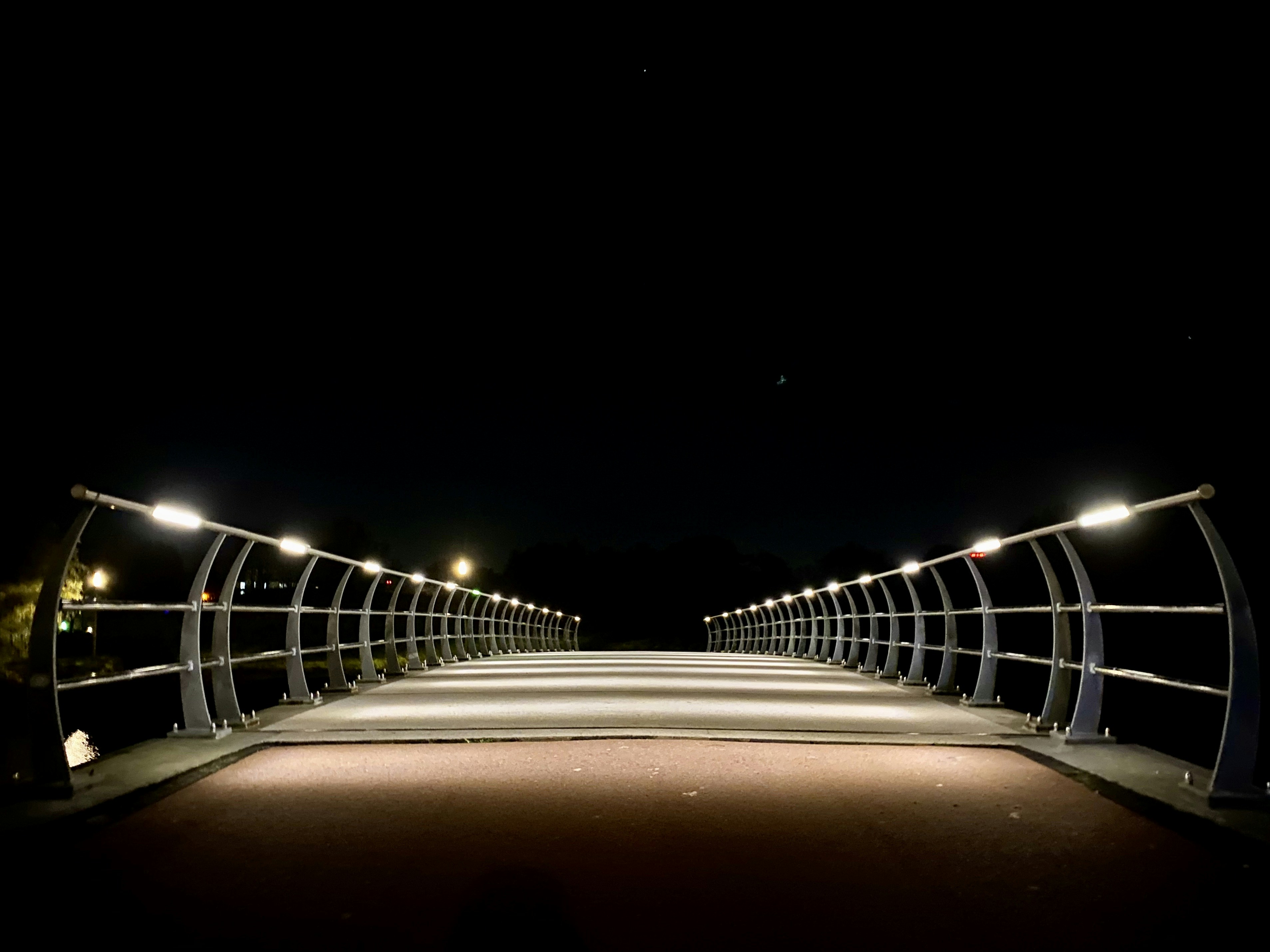 Arched bridge with glowing side lights against a dark night sky.