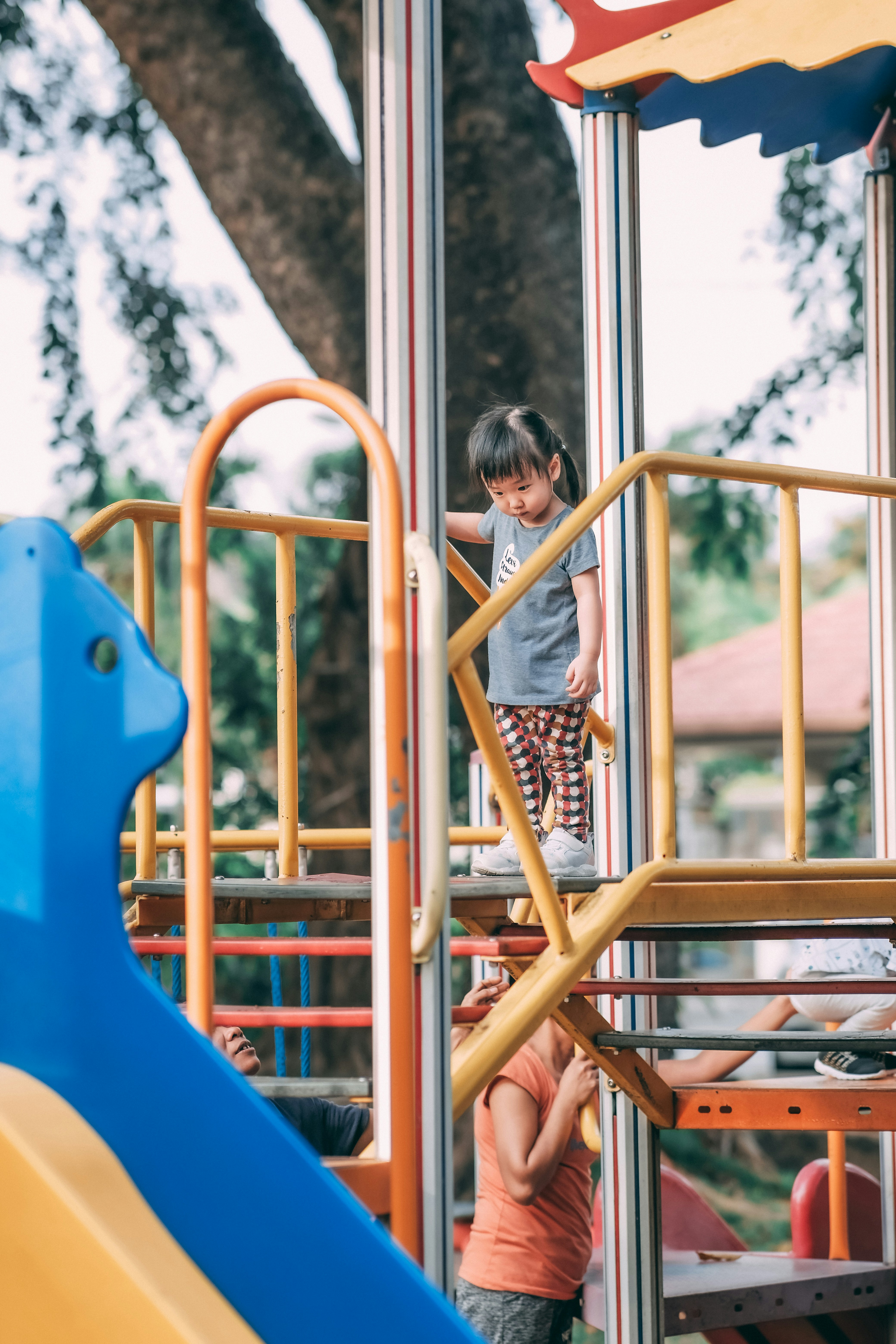 Girl in red and white floral dress climbing on blue slide during ...