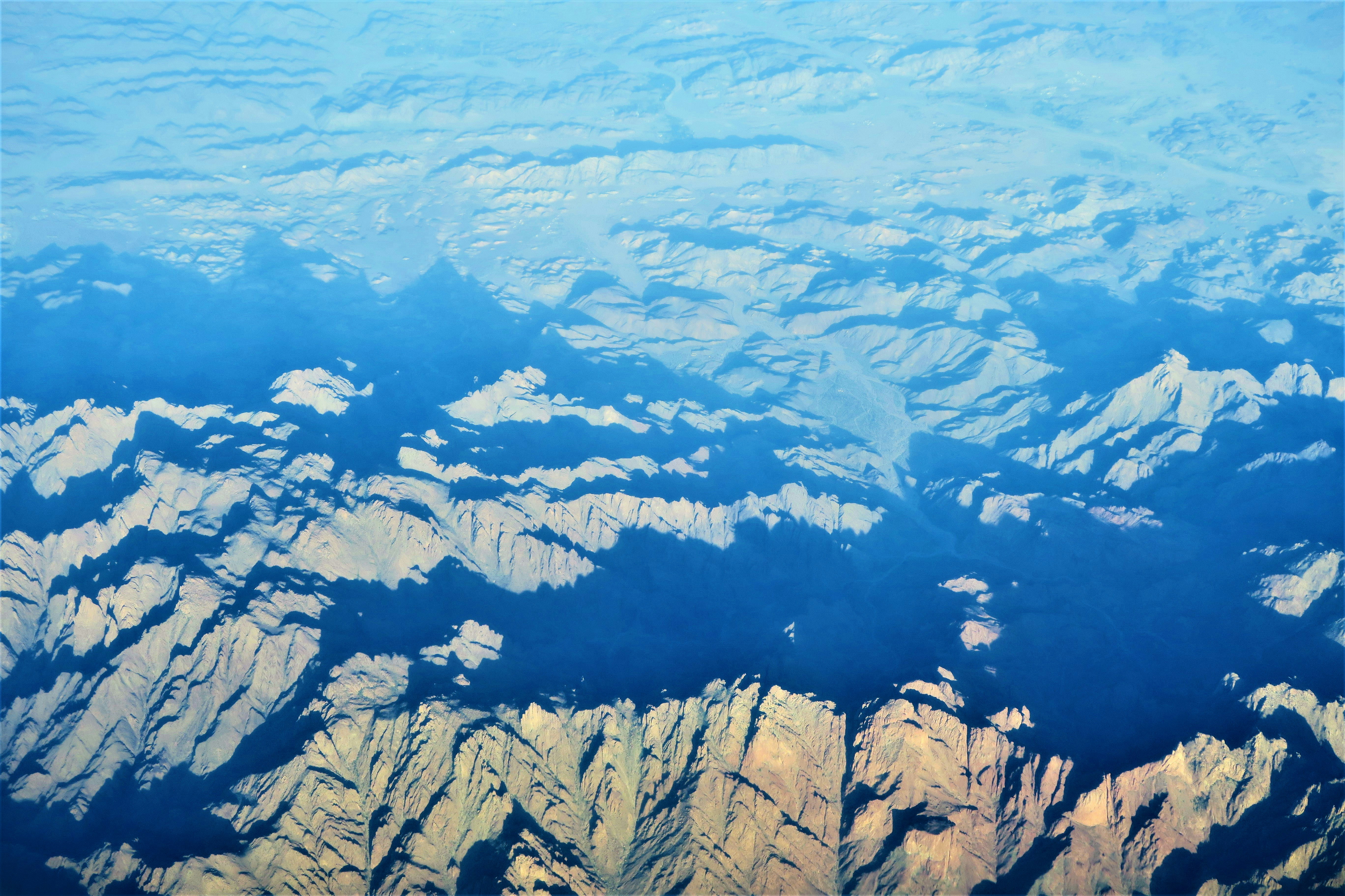 Aerial view of rugged mountain ranges bathed in soft blue light, accentuating the dramatic shadows and contours of the peaks.