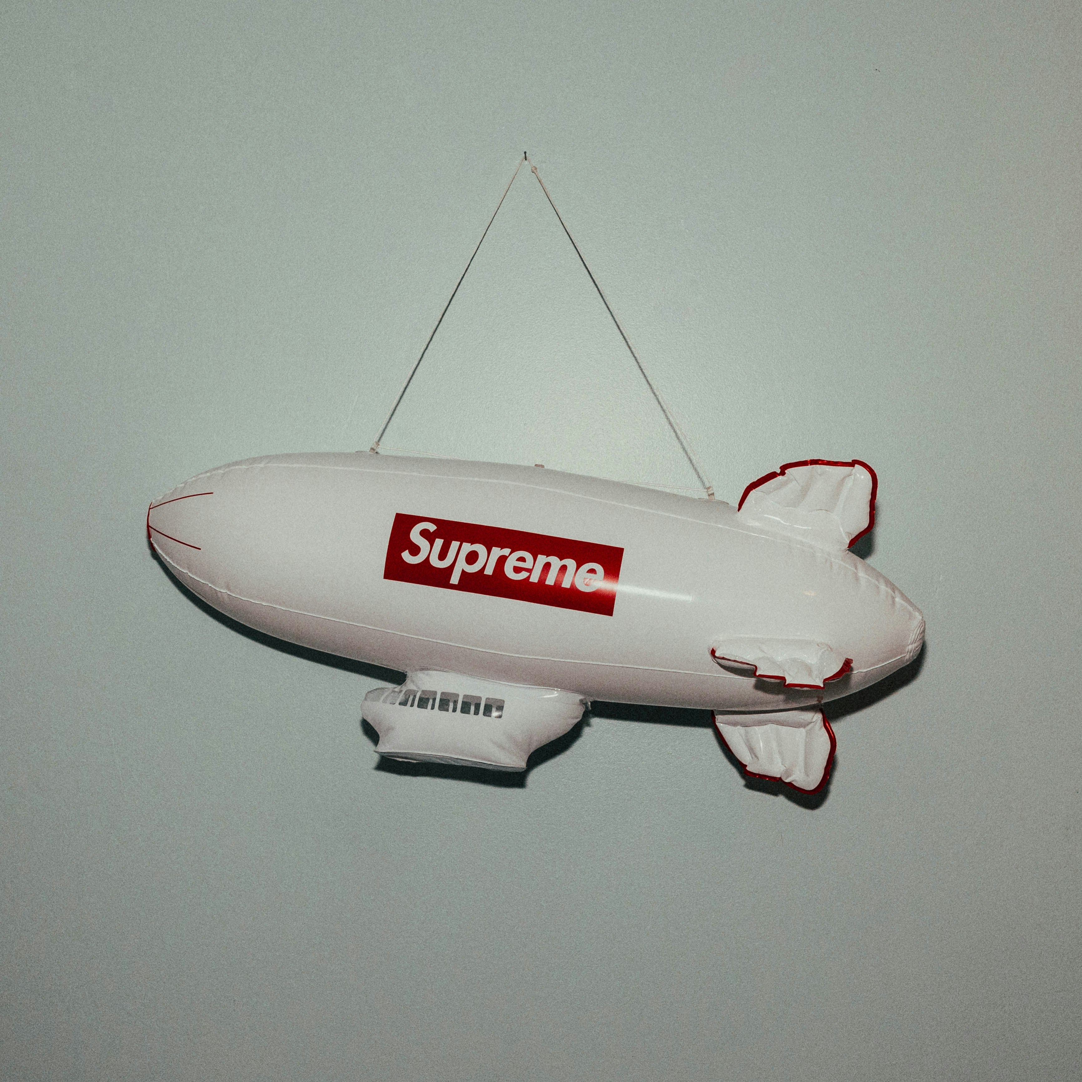 Inflatable zeppelin adorned with the Supreme logo, suspended against a neutral wall backdrop.