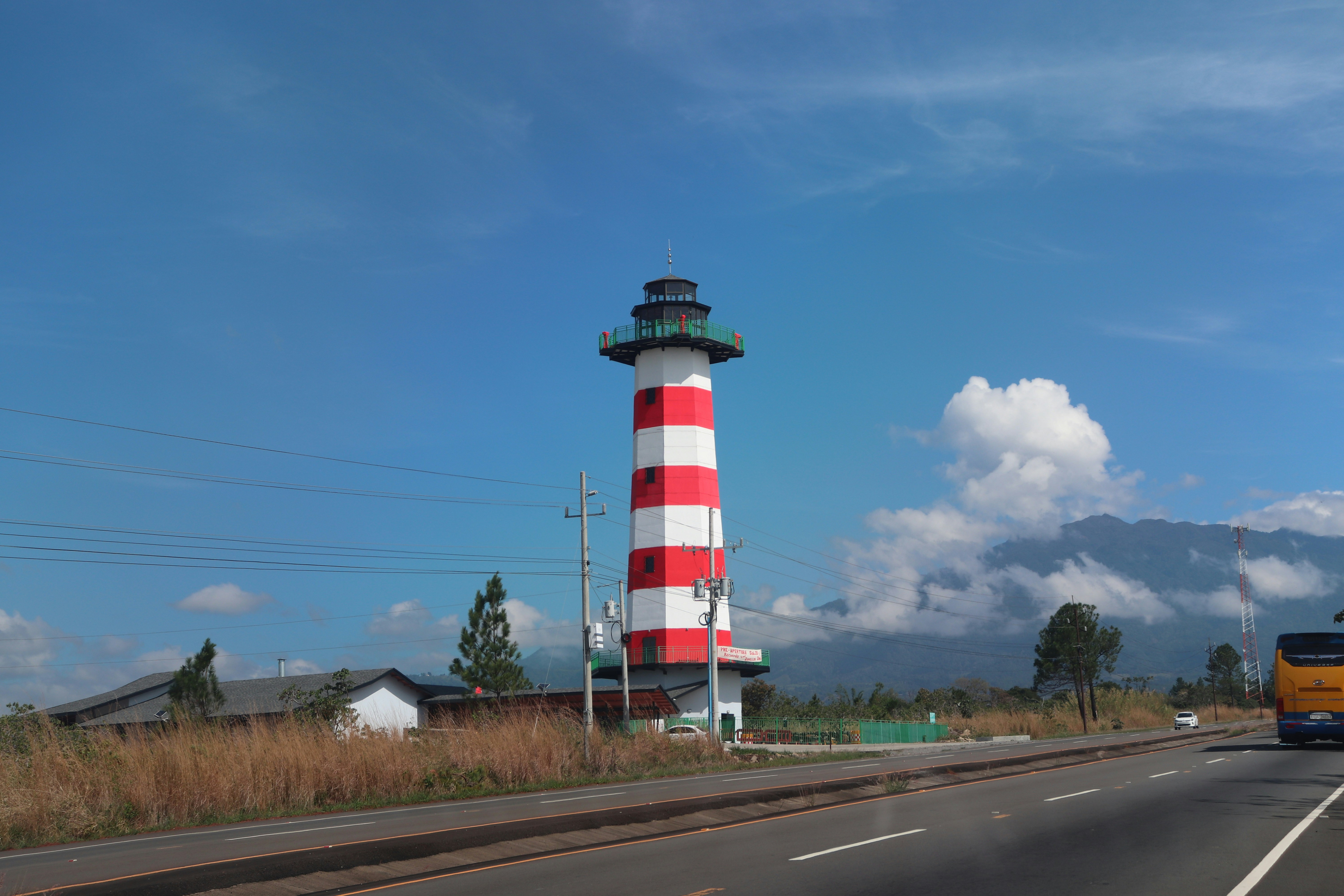 A vibrant red and white striped lighthouse standing tall against a backdrop of mountains and blue skies.