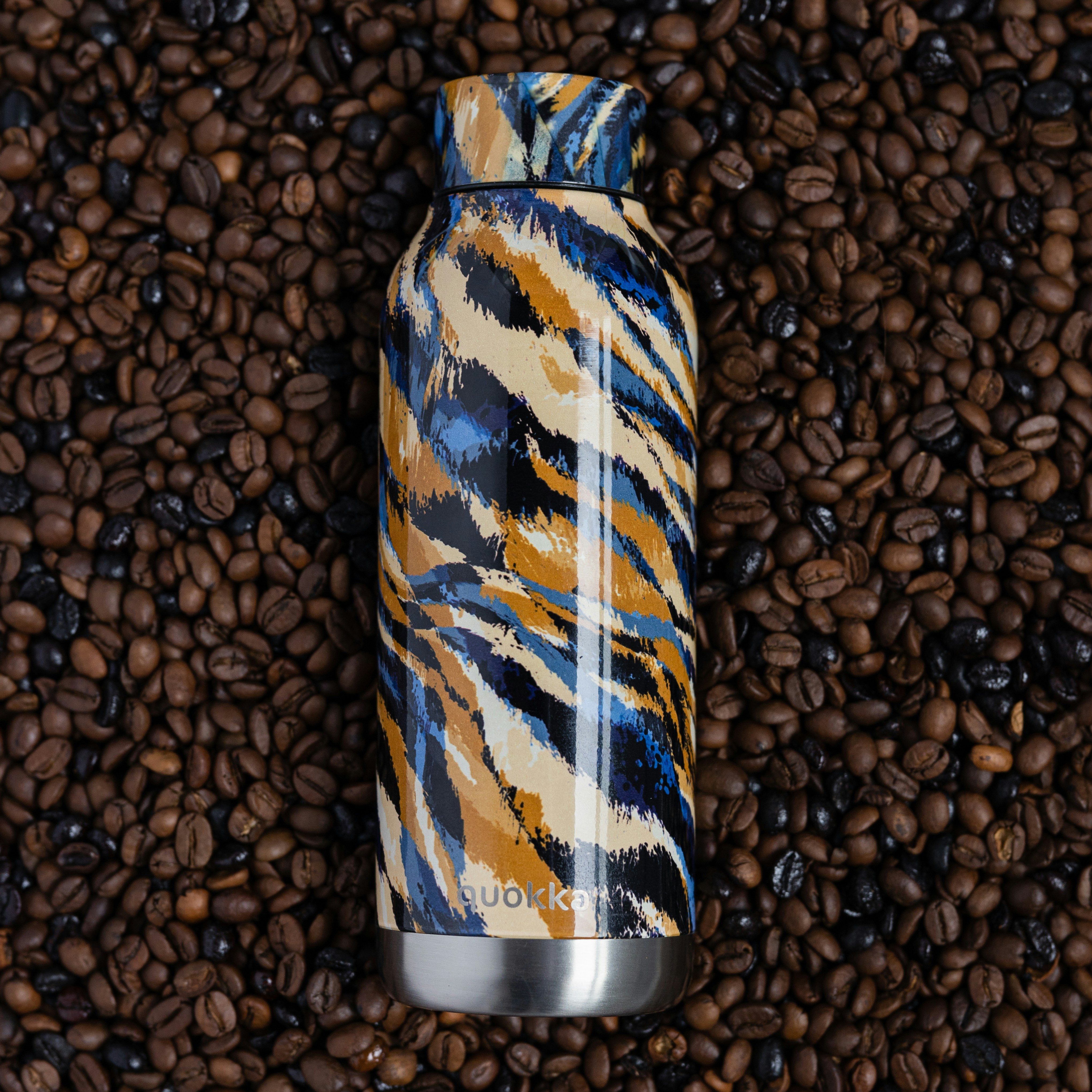Stylish insulated water bottle featuring a vibrant tiger stripe design, placed on a bed of roasted coffee beans.