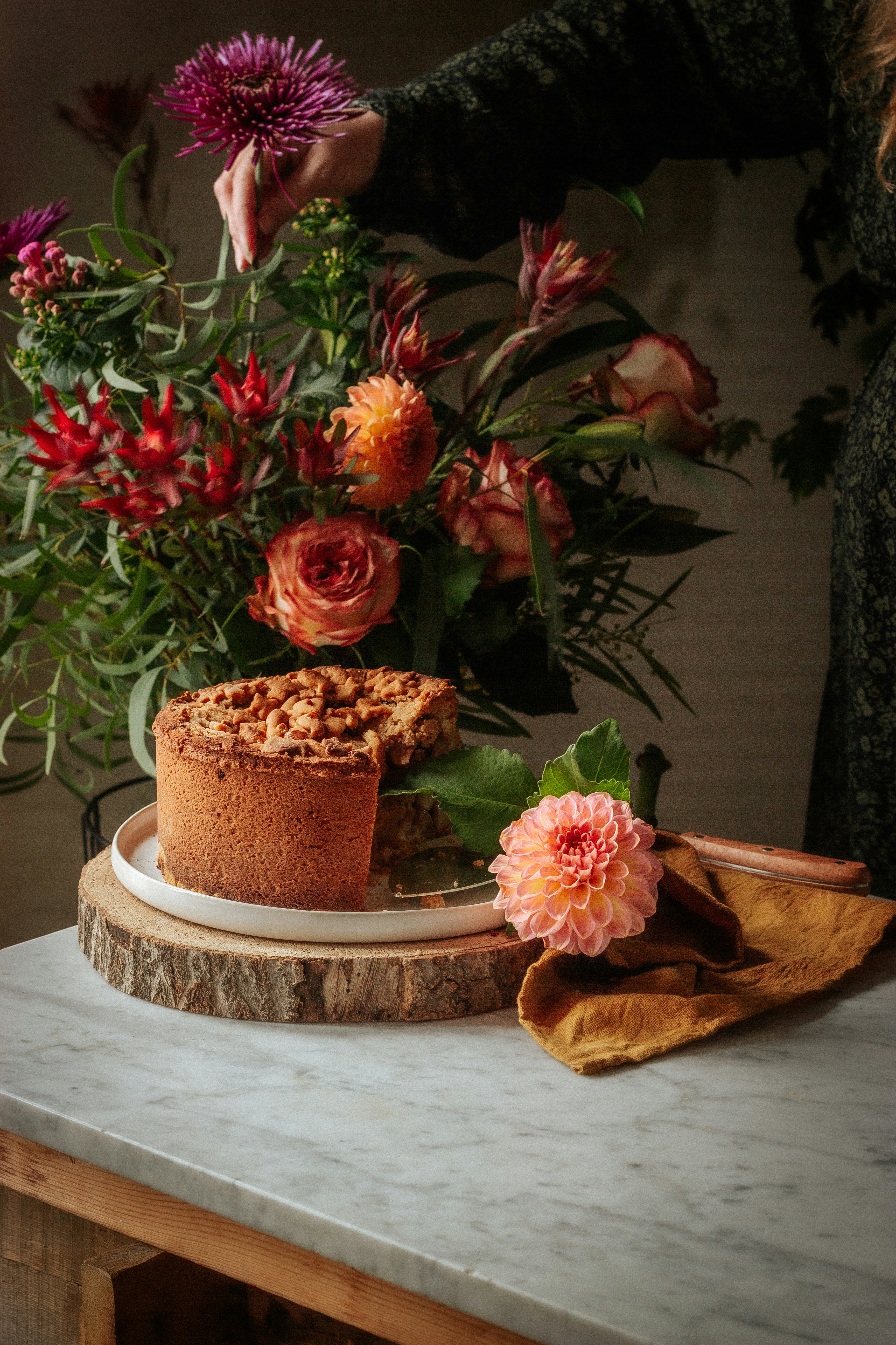 Caramel Cake on a Wooden Slab, Framed by a Lush Floral Arrangement
