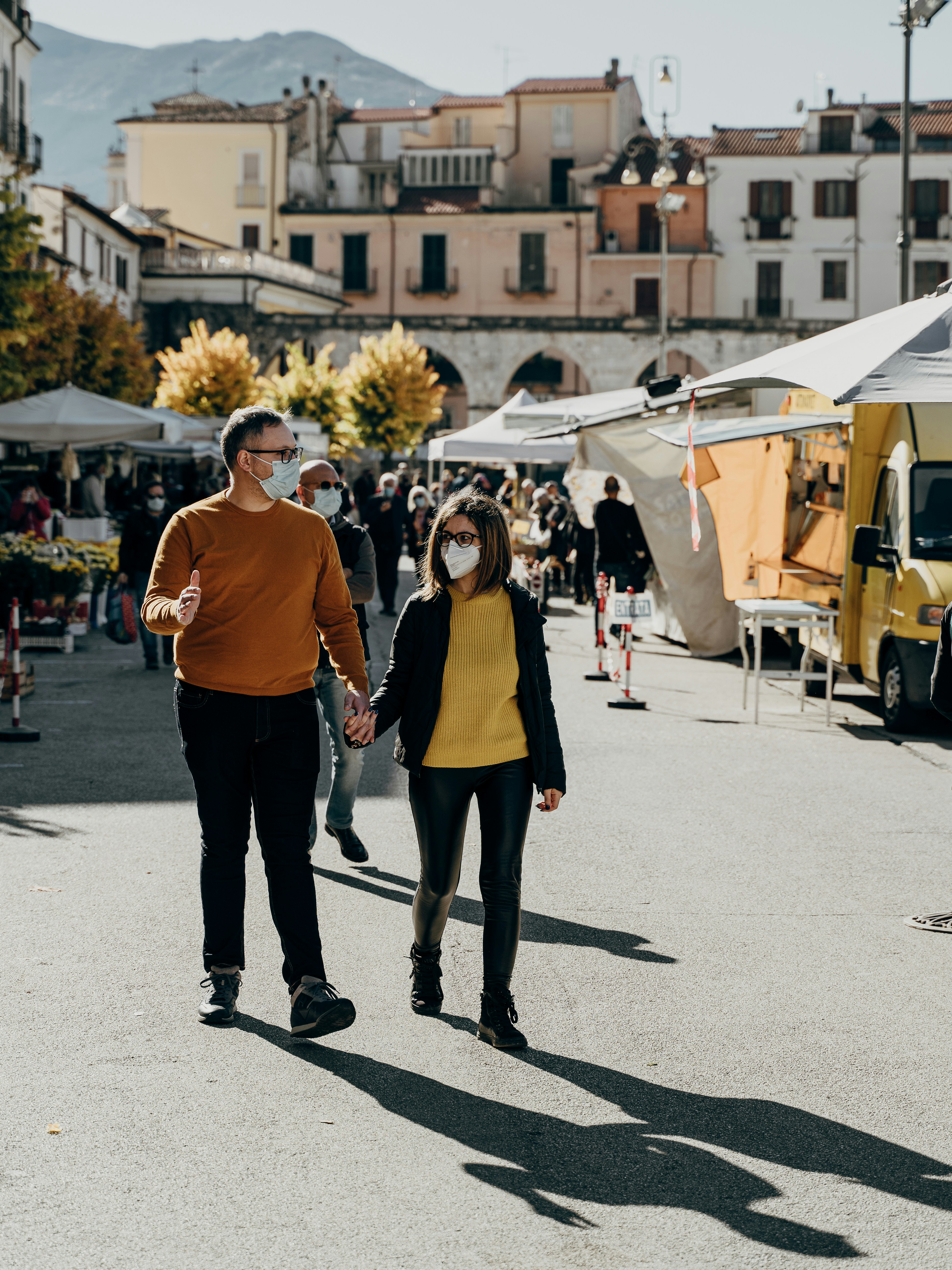 Sunlit Market Stroll: A Masked Couple Weaving Through a Busy Street Fair