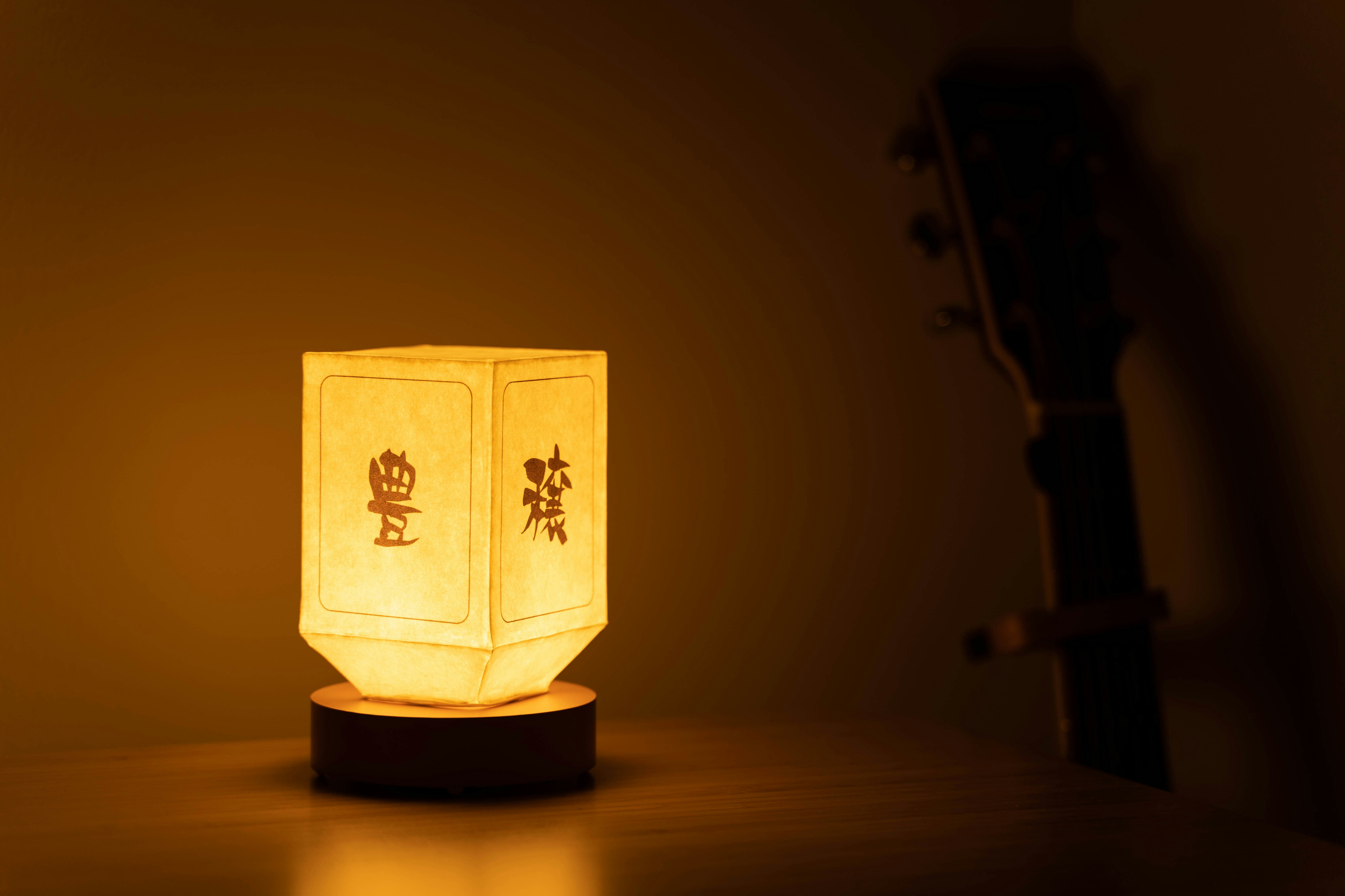 Lantern Glow on a Quiet Desk with a Shadowy Guitar in the Corner