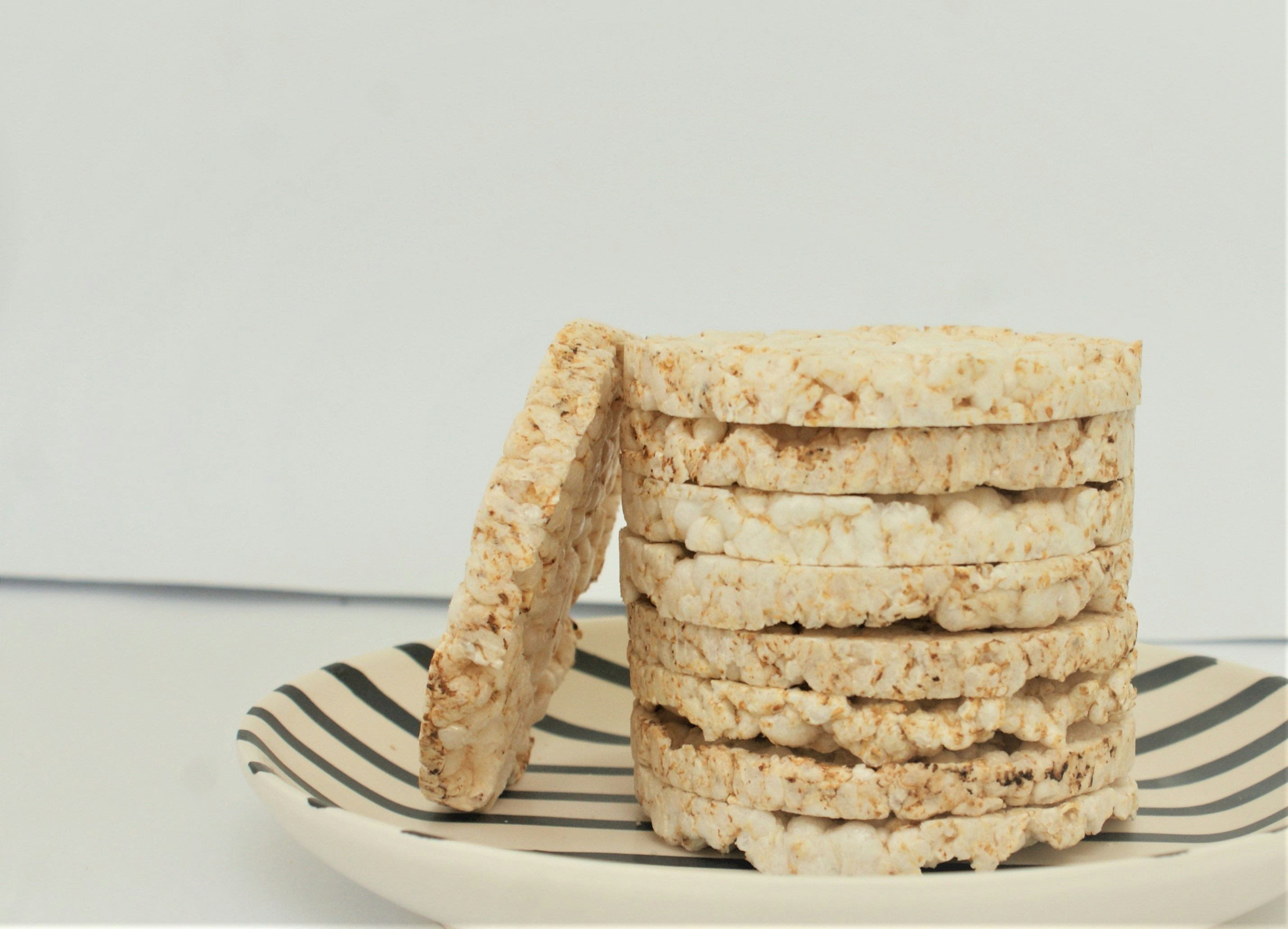 Stack of rice cakes arranged on a striped plate, showcasing their textured surfaces against a minimalistic backdrop.