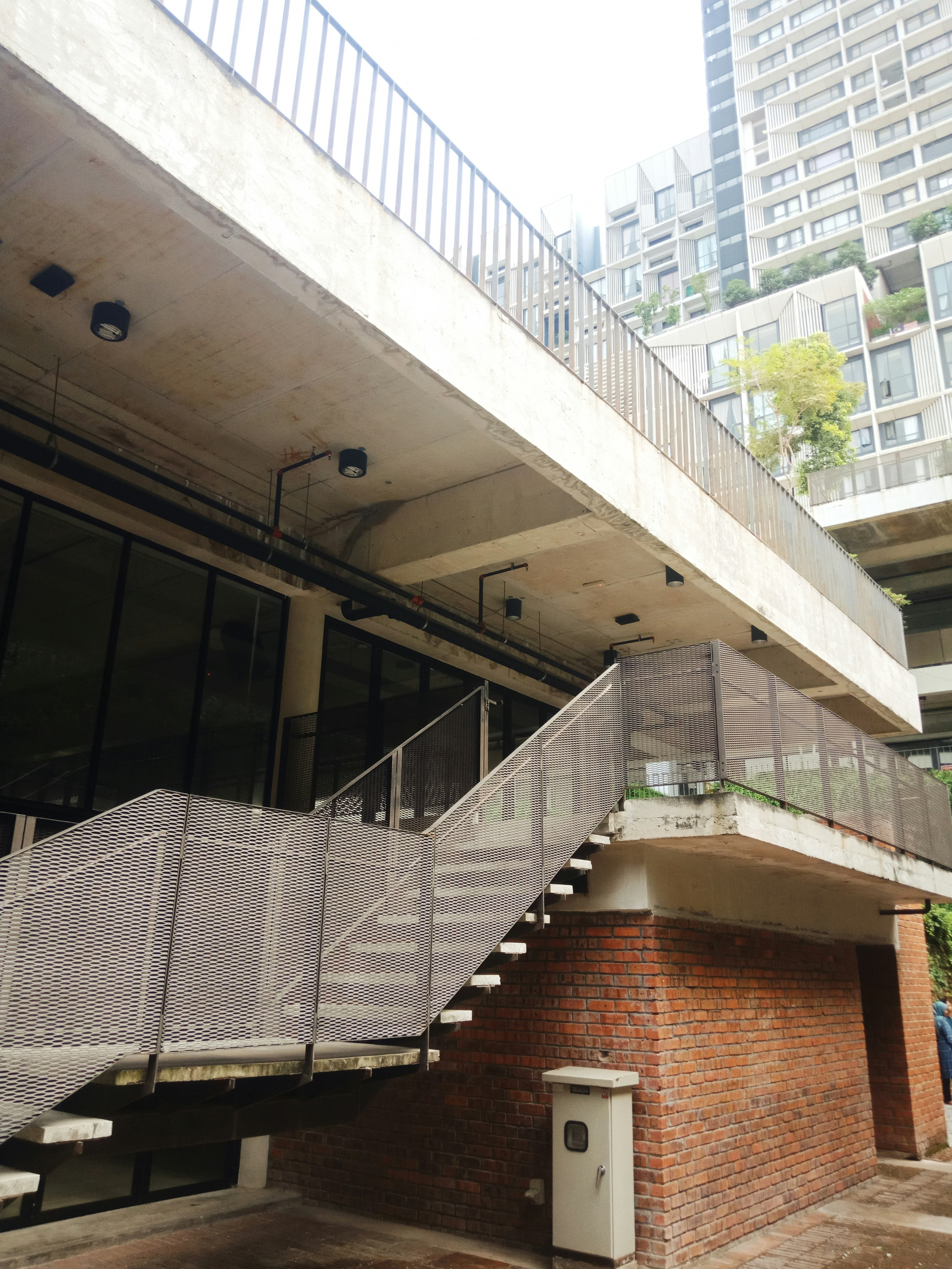 Industrial staircase leading to a modern building with a blend of concrete and glass architecture. The design emphasizes clean lines and functional aesthetics.