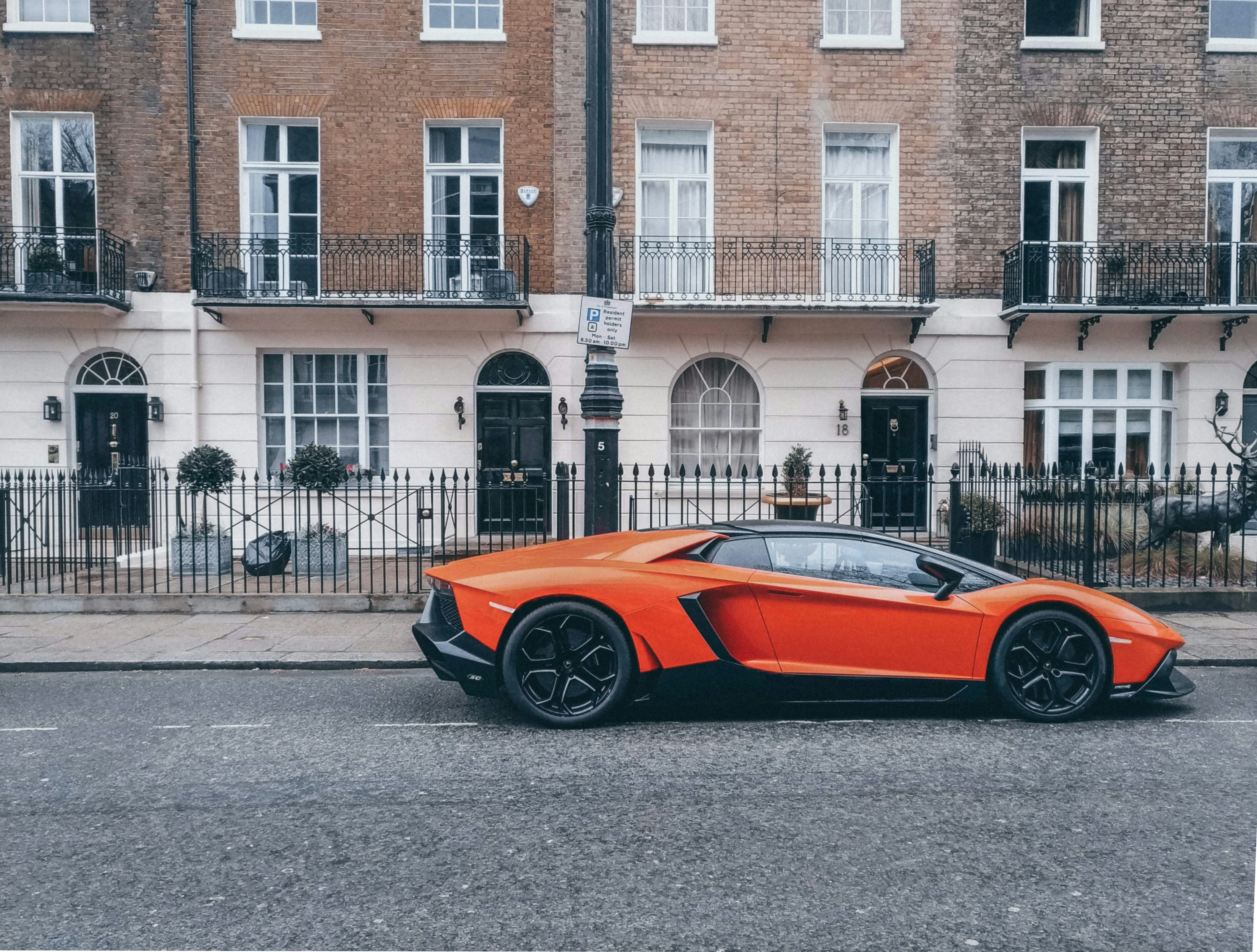 Orange sports car parked on a quiet city street with Georgian townhouses in the background—photograph.