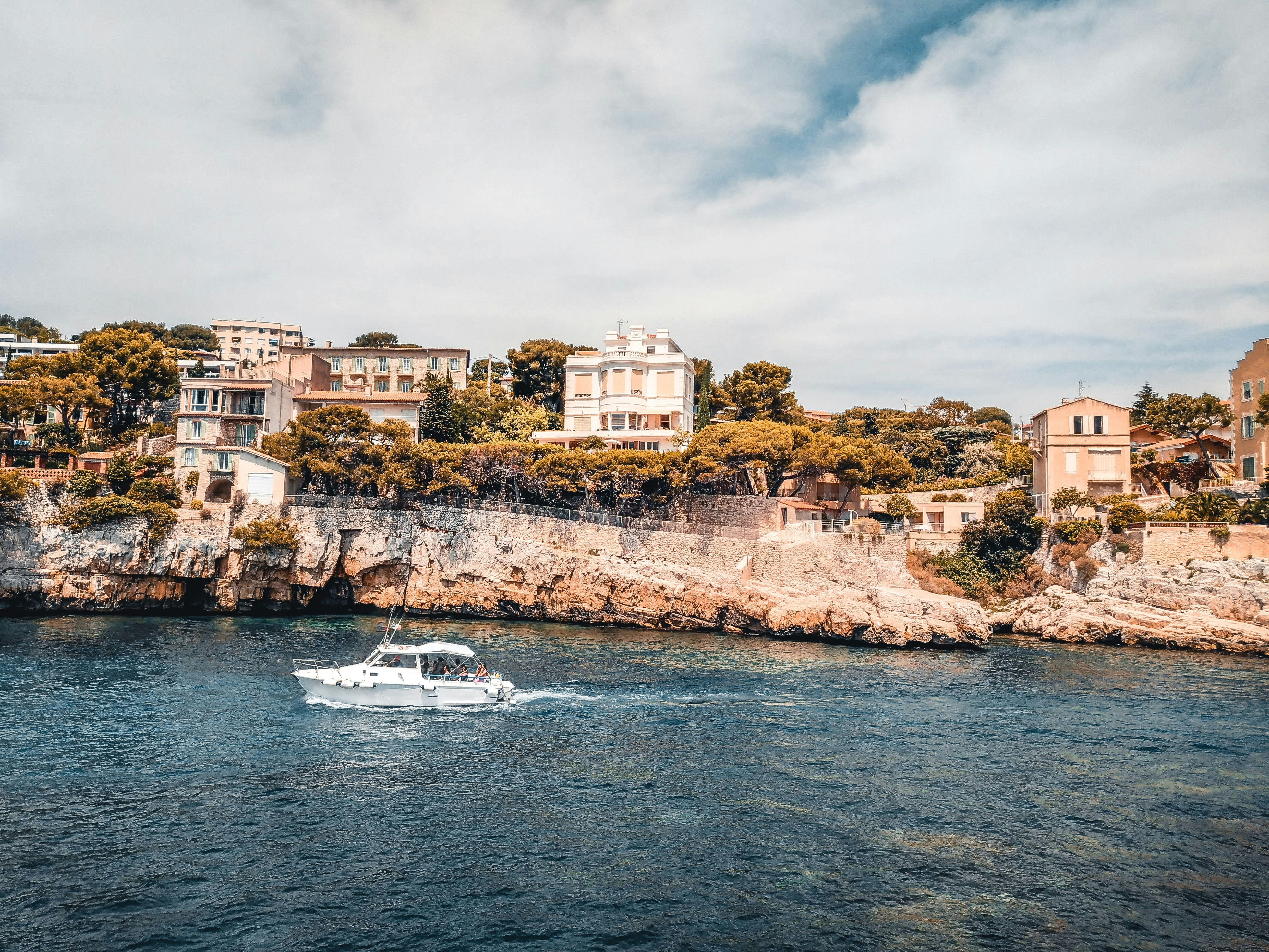 A motorboat glides through calm waters near a picturesque coastal village, surrounded by lush greenery and charming homes.