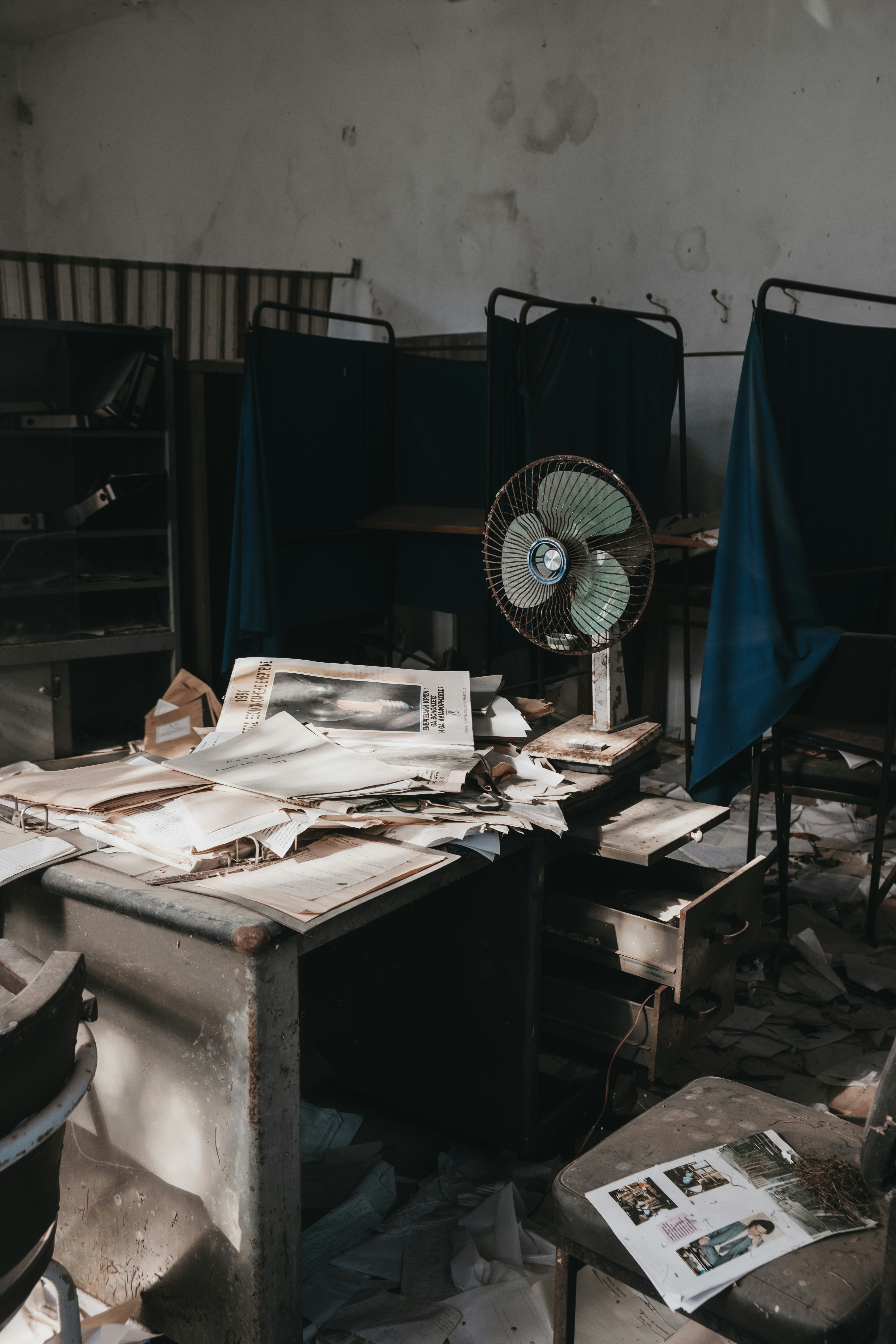 An abandoned room filled with scattered papers and a vintage fan, evoking a sense of nostalgia and neglect.