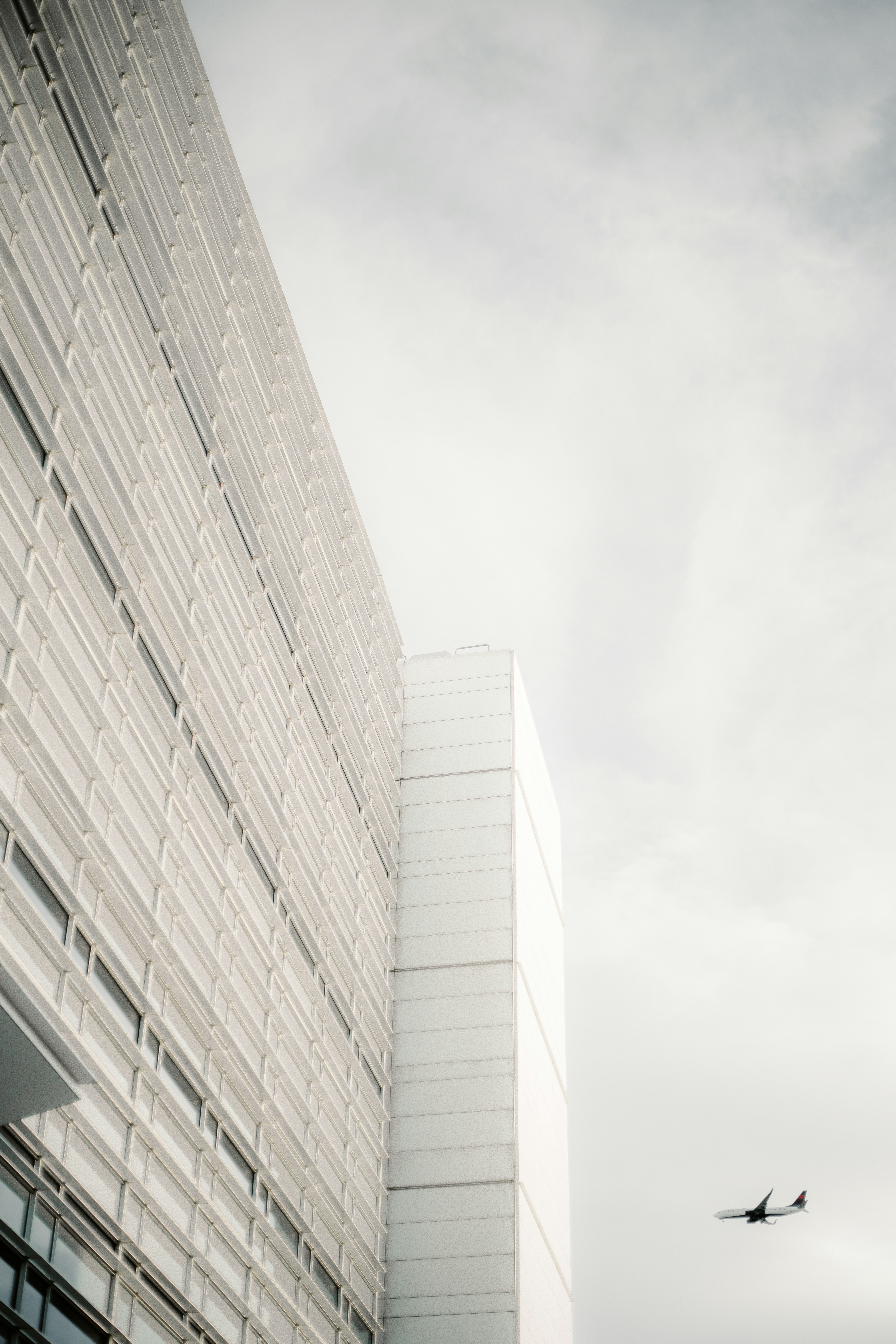 Modern building facade juxtaposed with an airplane in flight against a cloudy sky.