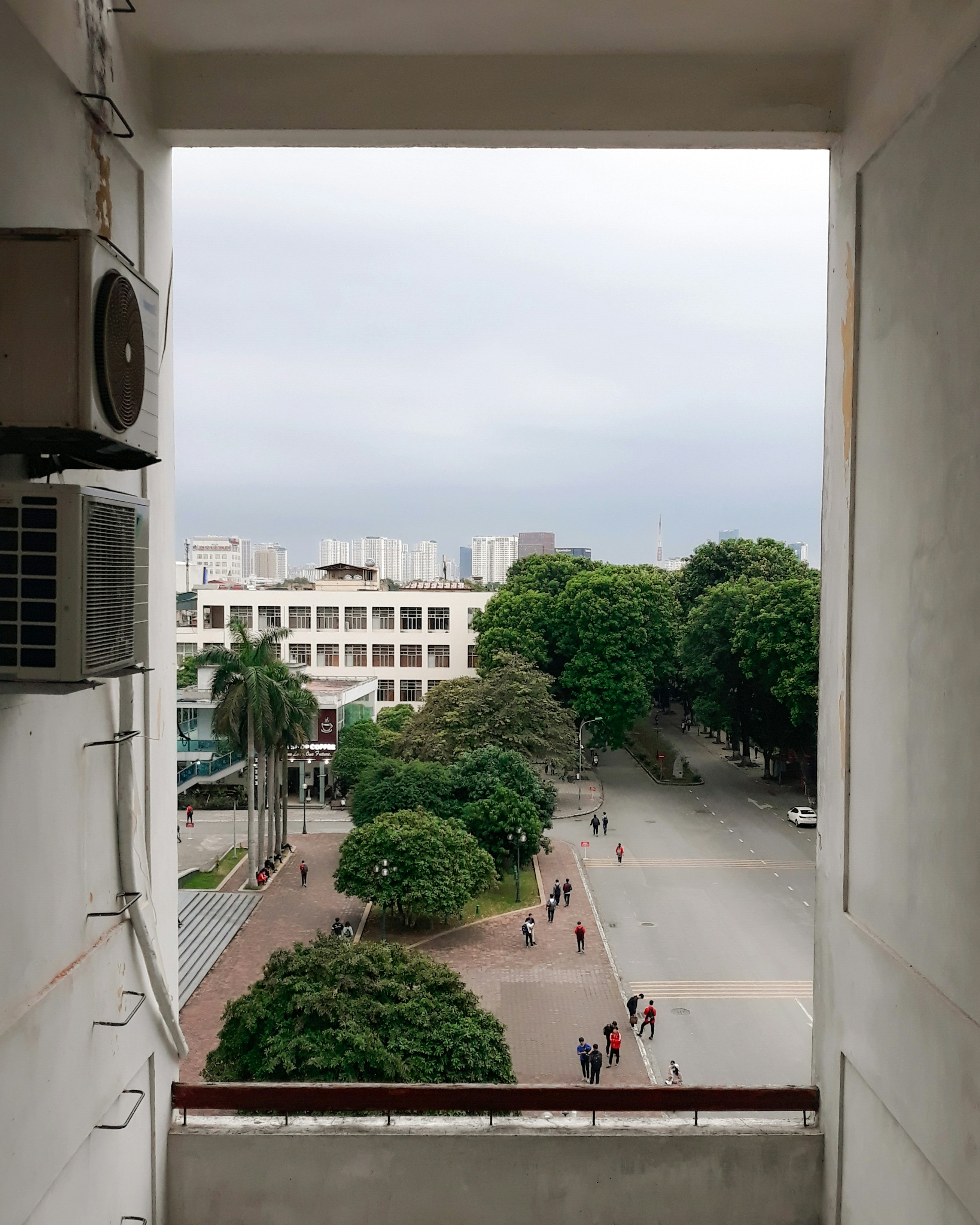 View from a window showcasing a tree-lined street with pedestrians and buildings in the background. The scene captures urban life framed by the window's architecture.