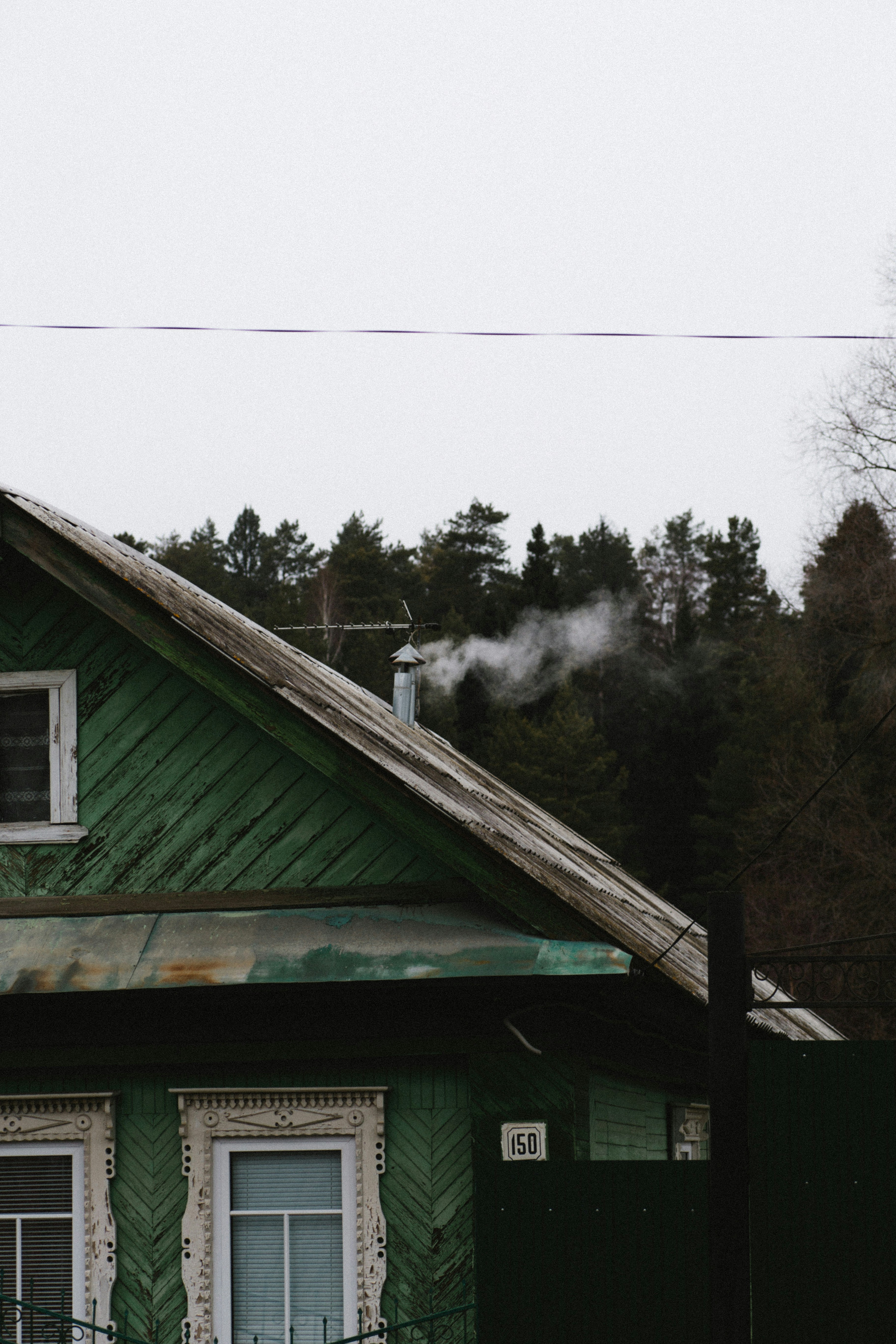 Charming green cottage with smoke curling from the chimney, surrounded by a tranquil forest backdrop.