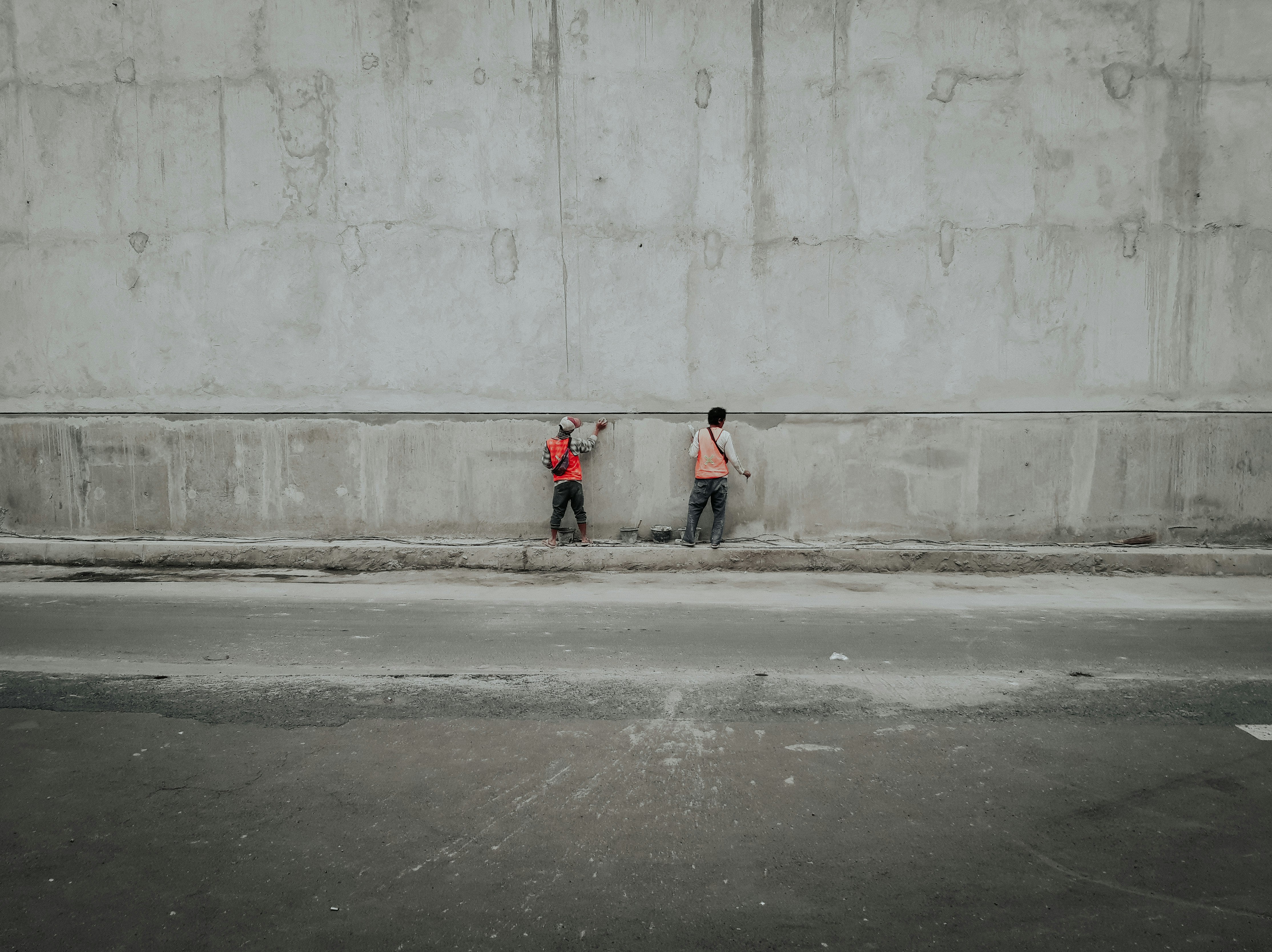 Two children playing against a large concrete wall beside an empty urban street.