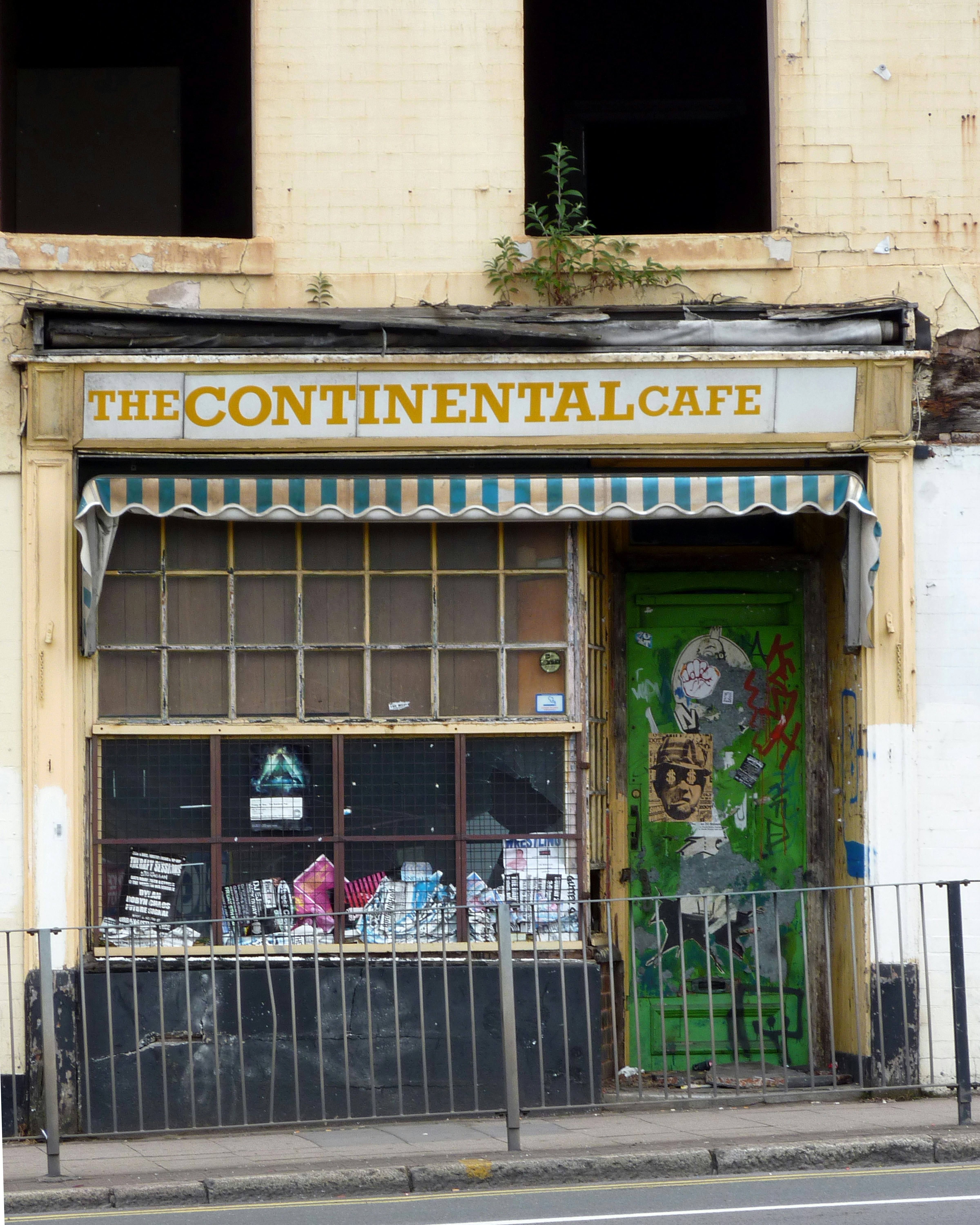 Weathered café facade with a vibrant green door and peeling signage, showcasing urban decay and remnants of past life.