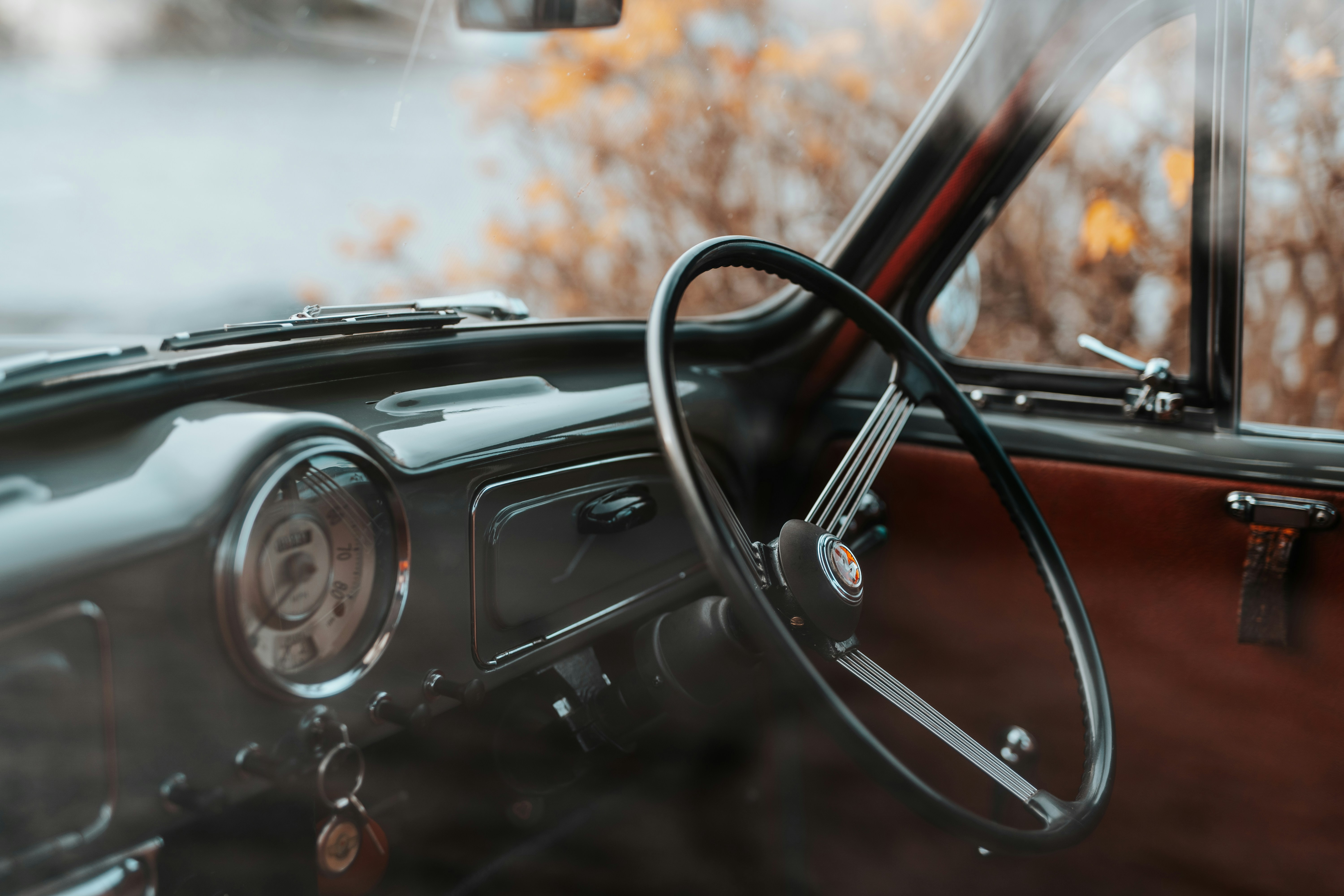 Classic car interior with a vintage steering wheel and dashboard, surrounded by autumn foliage.