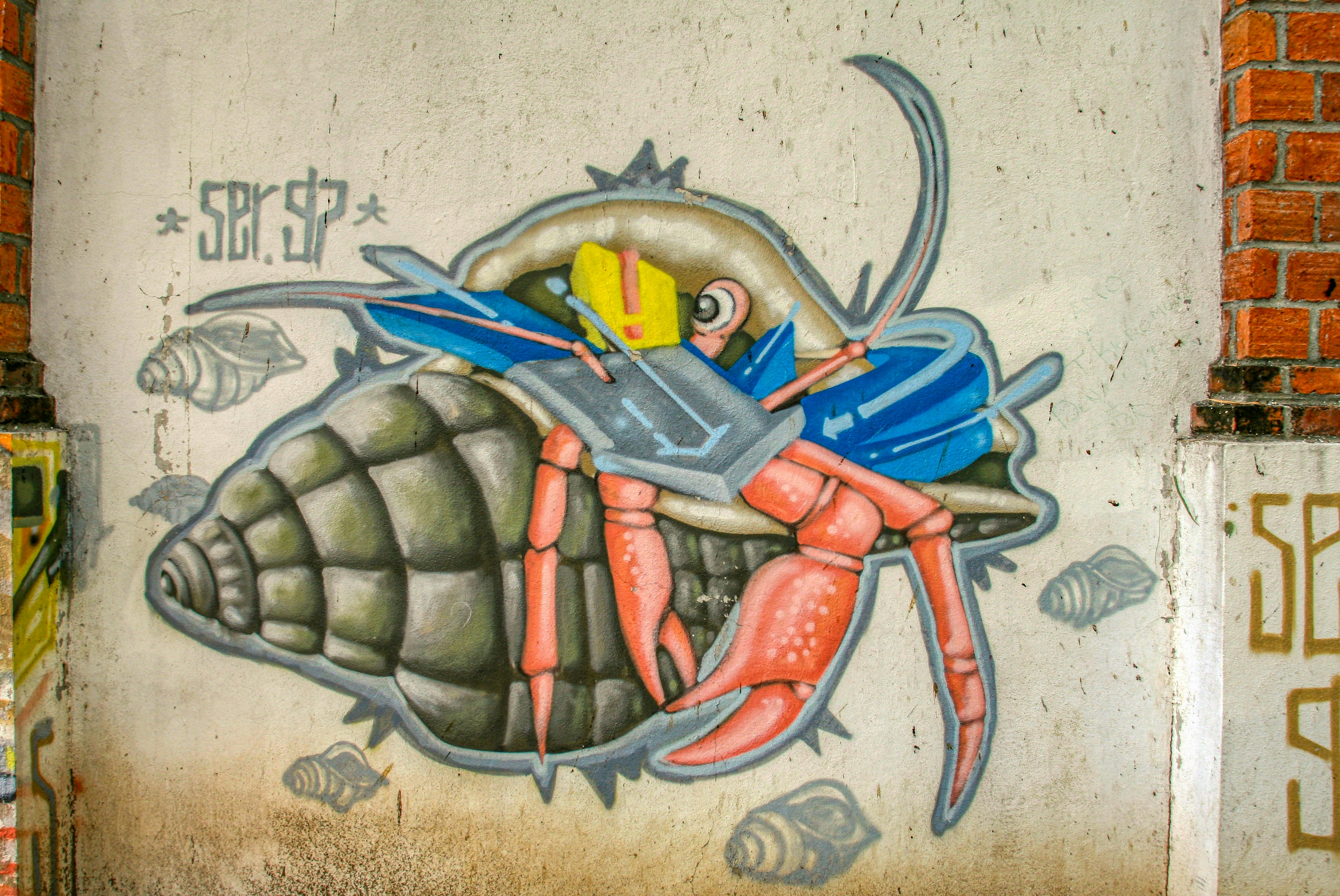 Colorful hermit crab mural blending urban elements with marine life on a concrete wall.