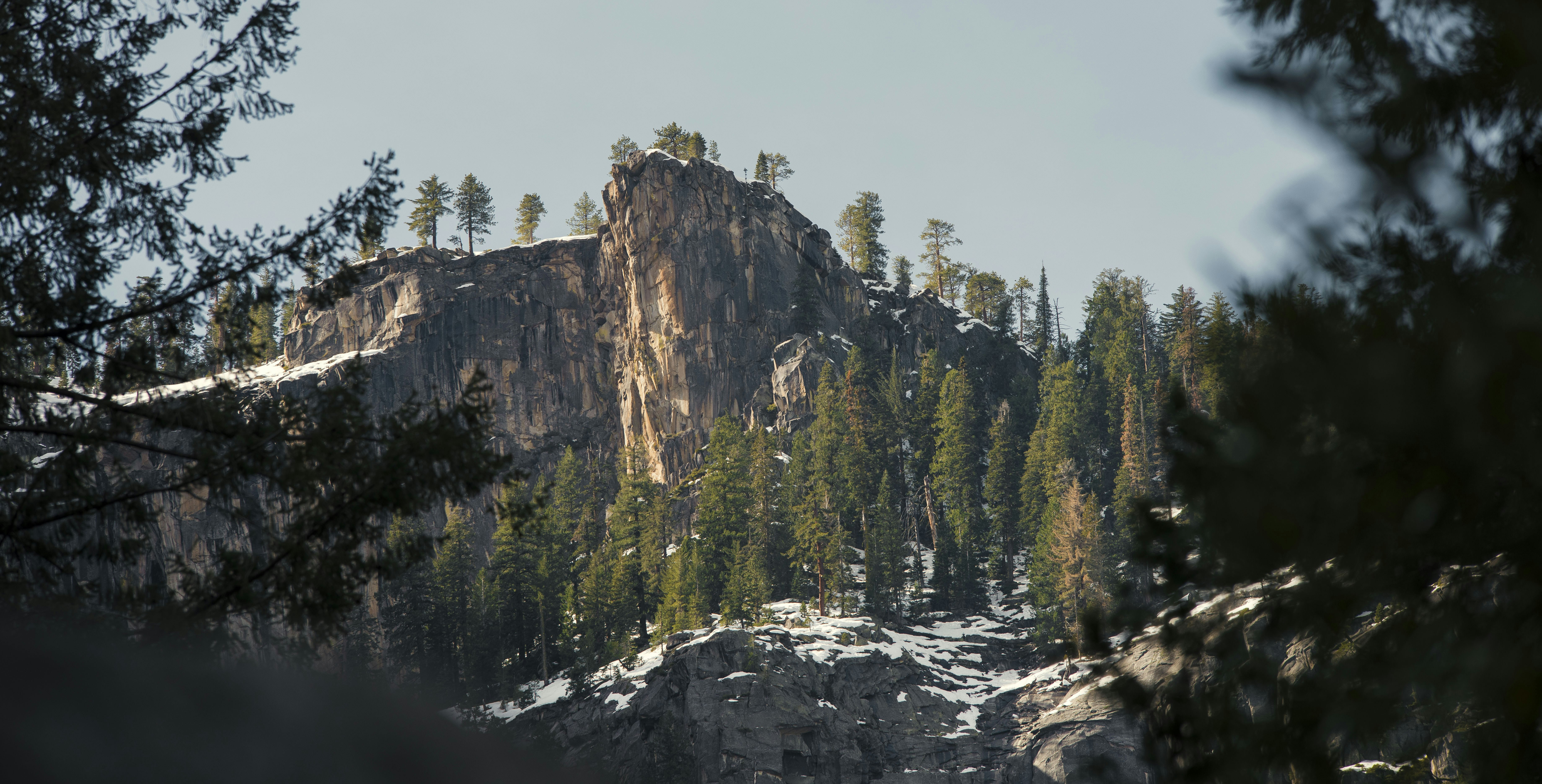 Sunlit granite peak framed by evergreen trees and patches of snow in Yosemite.