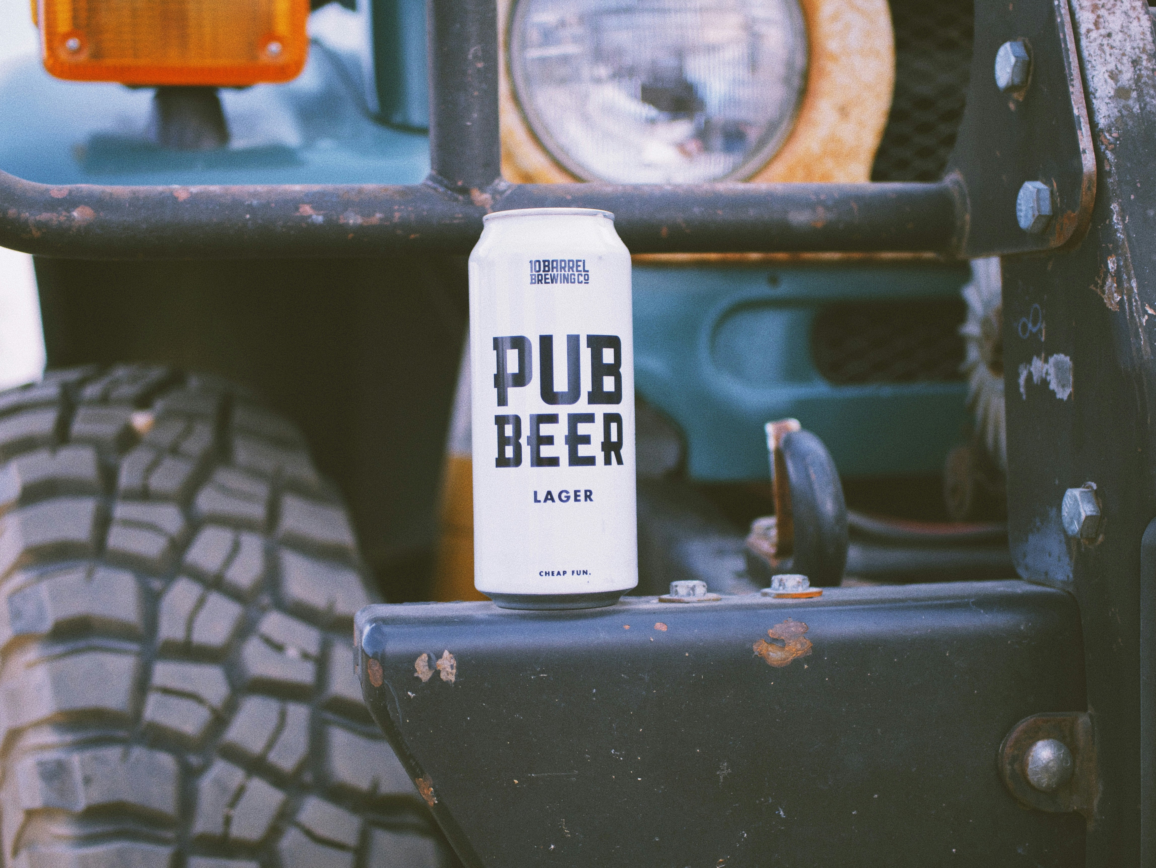 A can of PUB BEER lager rests on the rugged frame of a vehicle, showcasing a blend of outdoor spirit and casual enjoyment.