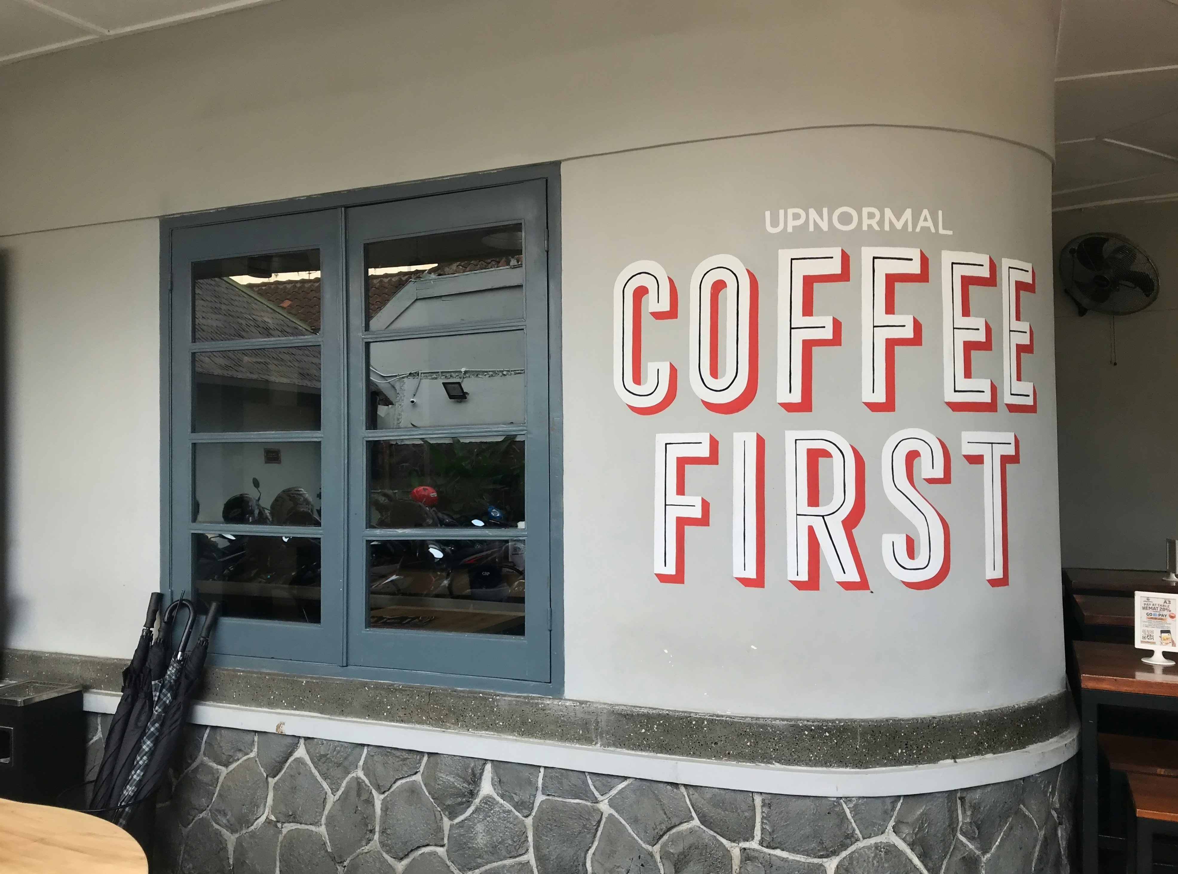 Café wall with bold 'Coffee First' lettering beside a window with blue shutters.