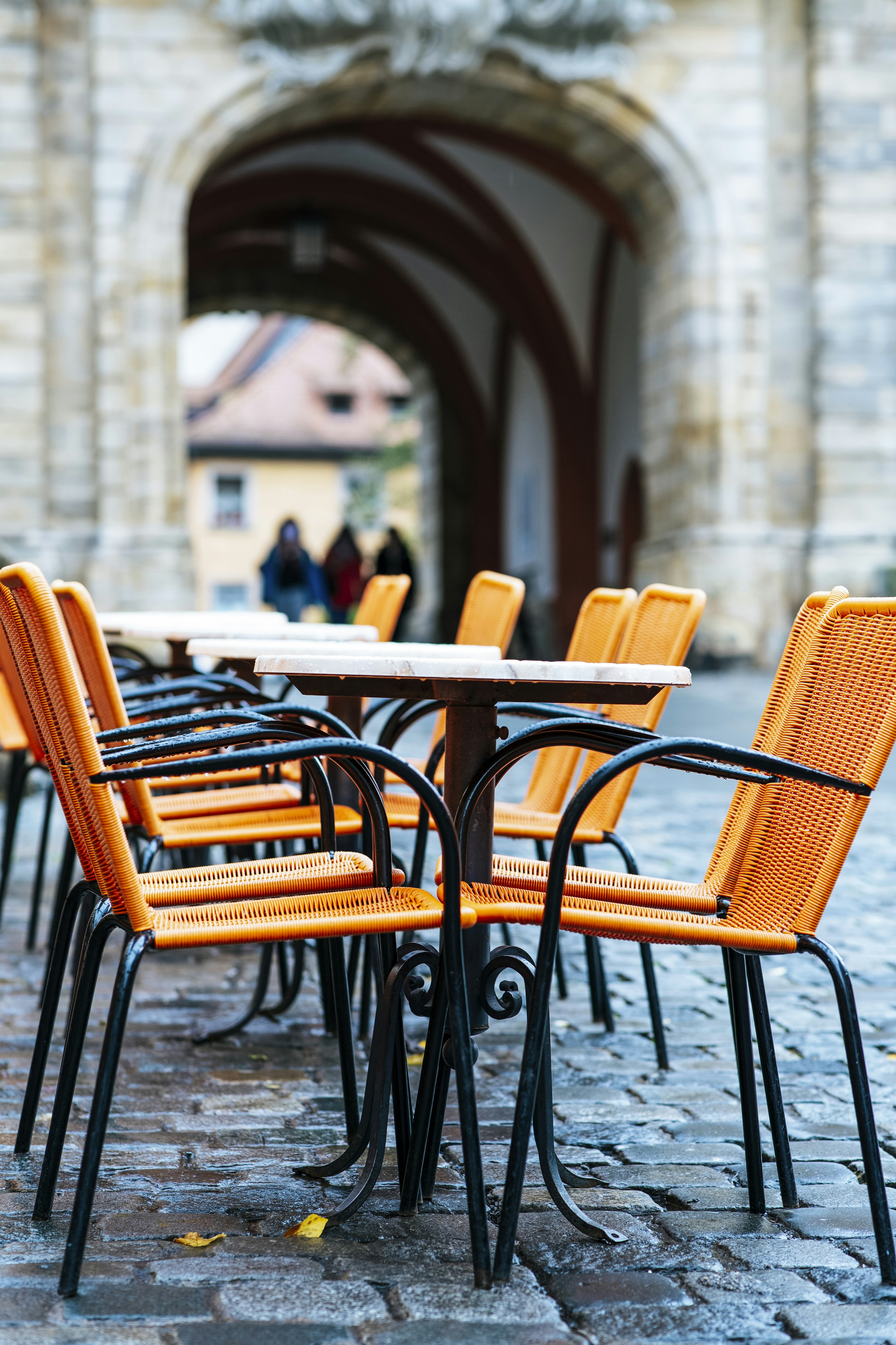 Orange Chairs on a Cobblestone Passage under a Stone Arch
