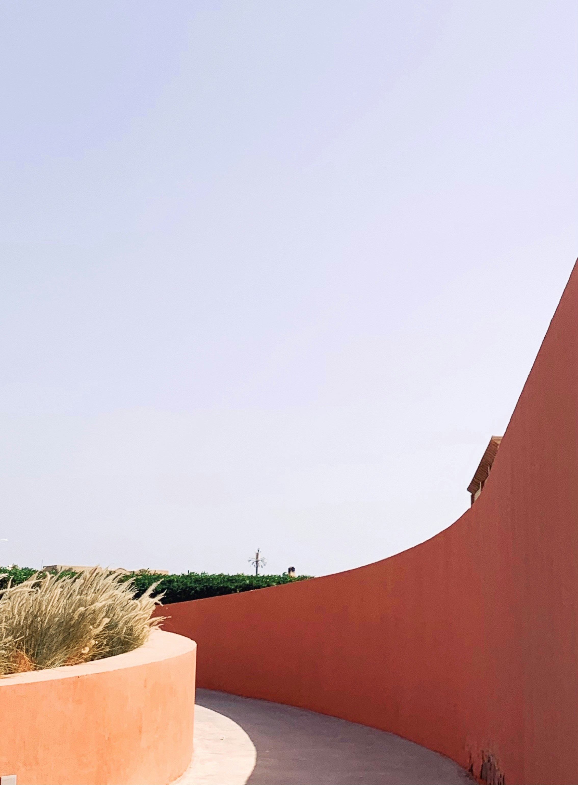 A winding pathway bordered by vibrant orange walls and lush greenery under a clear sky.