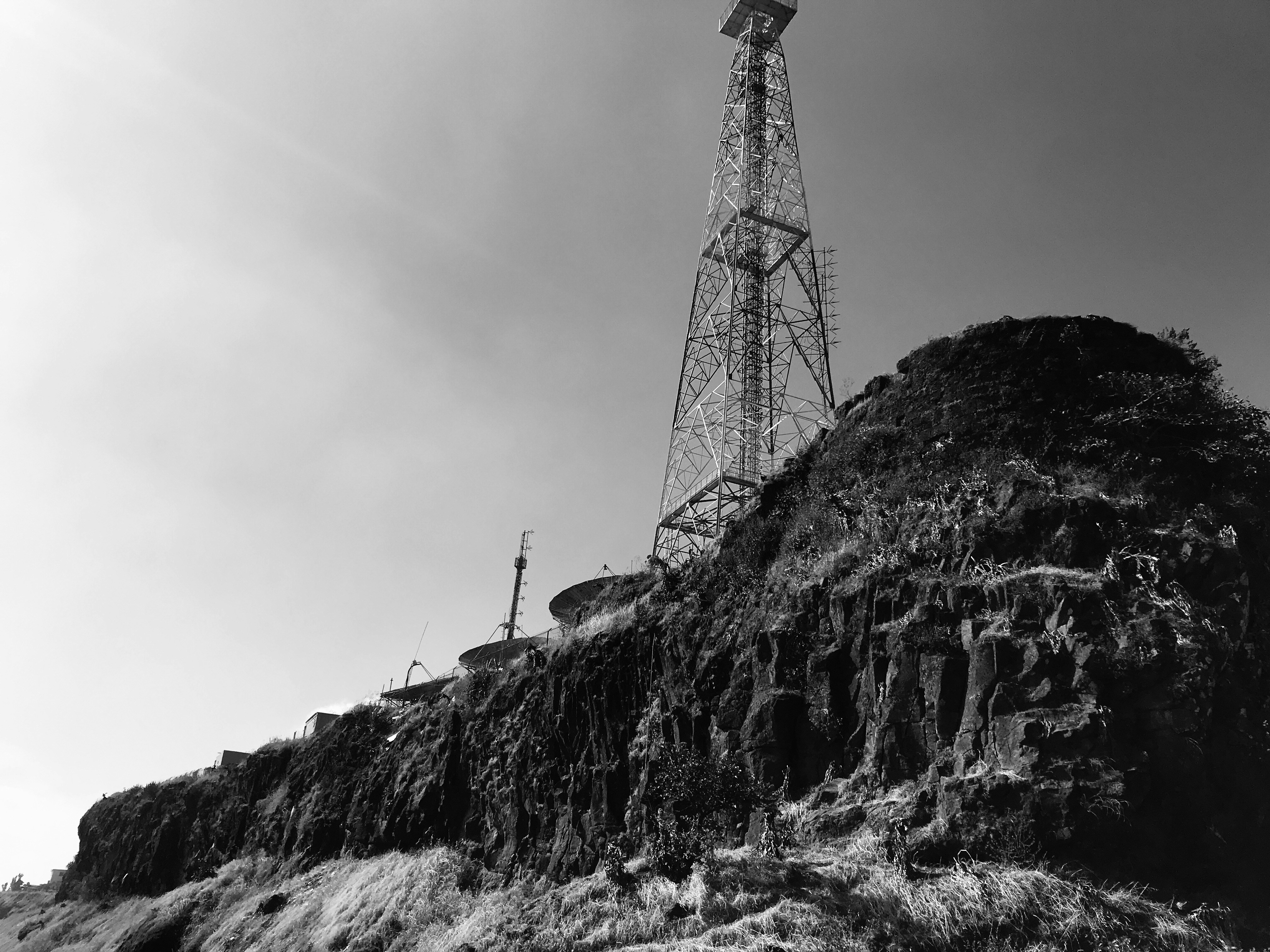 Grayscale windmill standing tall on a rugged hill under a vast sky.