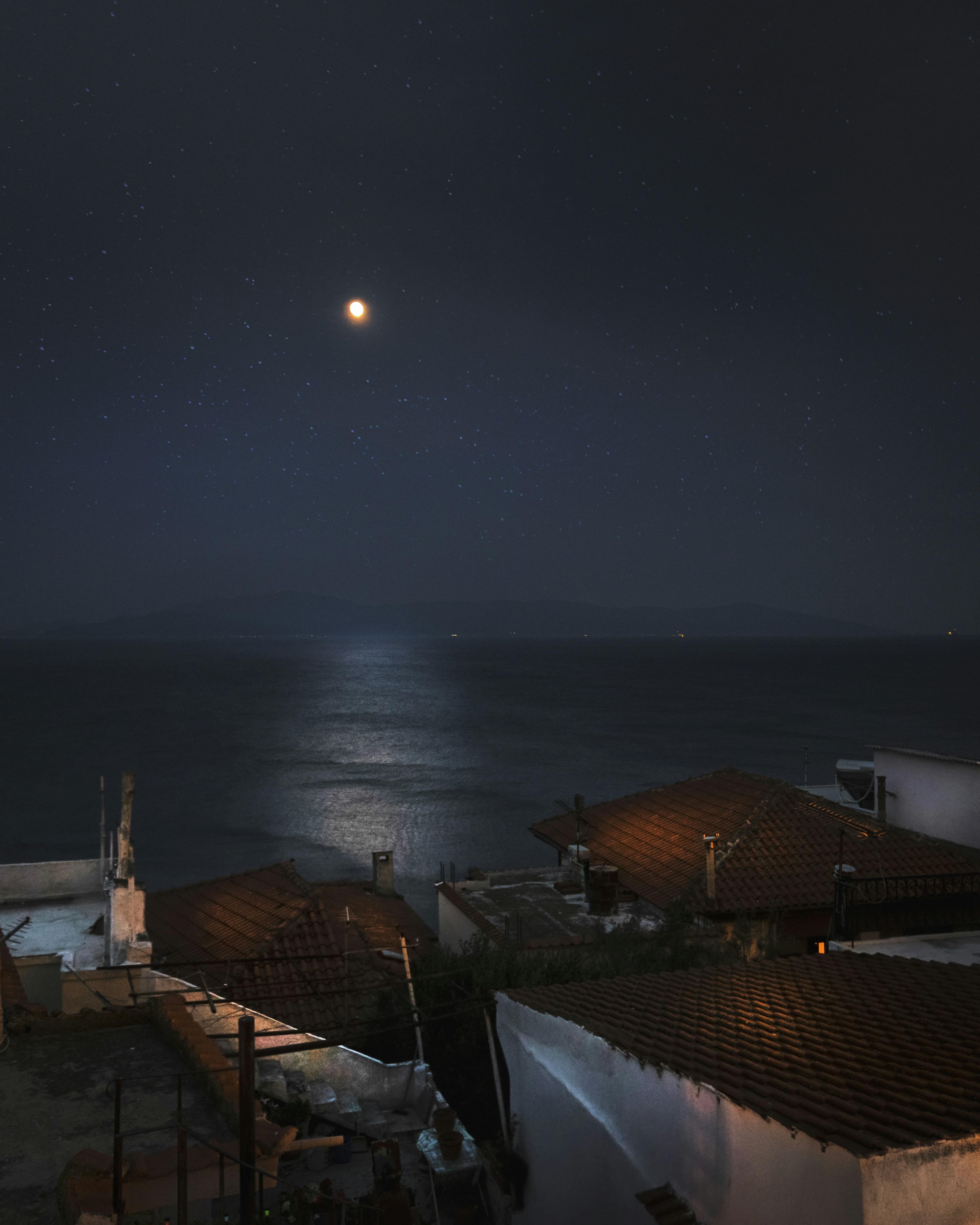 Moonlit Night Over Rooftops: Calm Sea Reflections