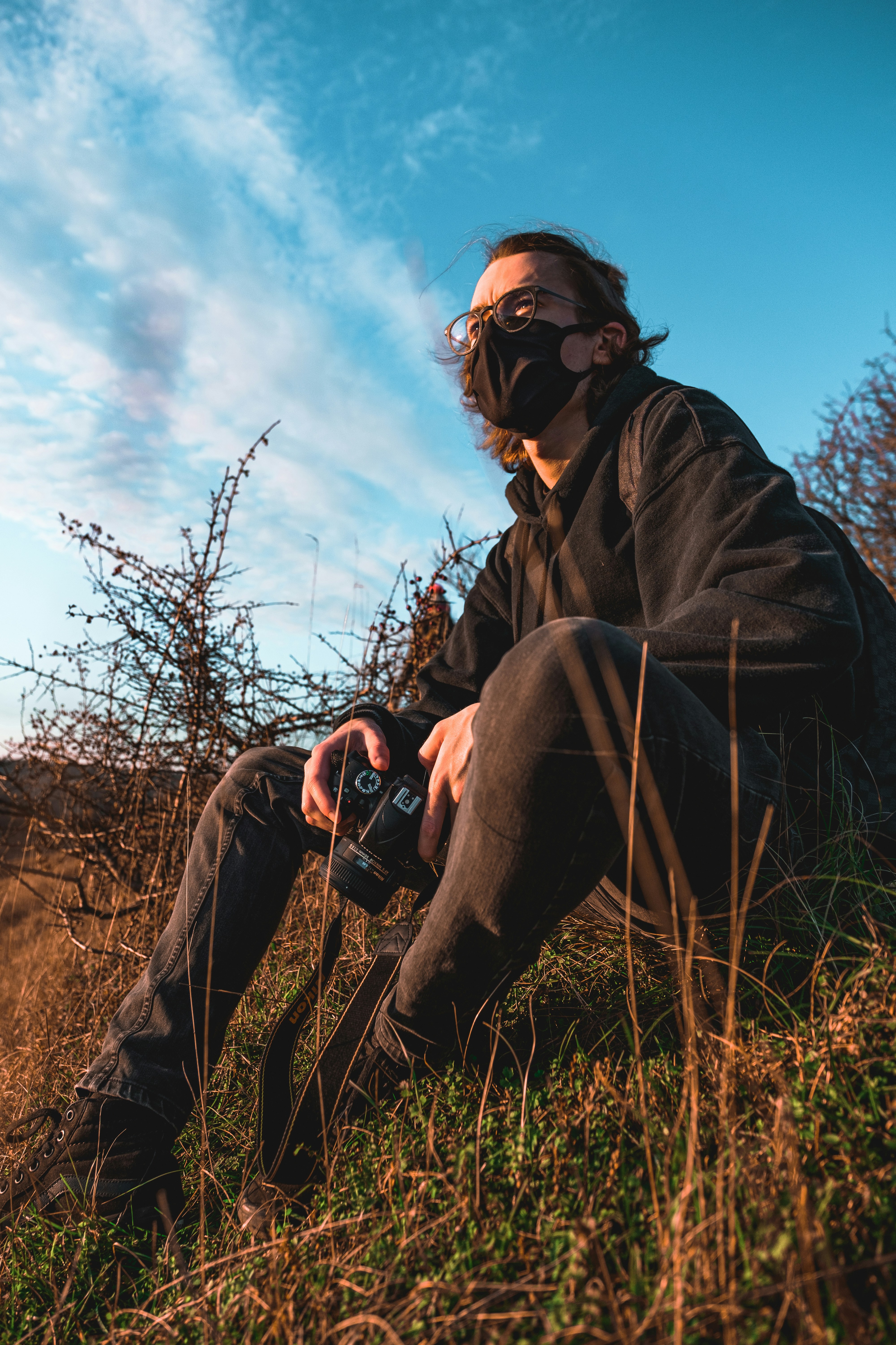 Cerulean Sky Rendezvous: A Masked Photographer Poised on the Hillside