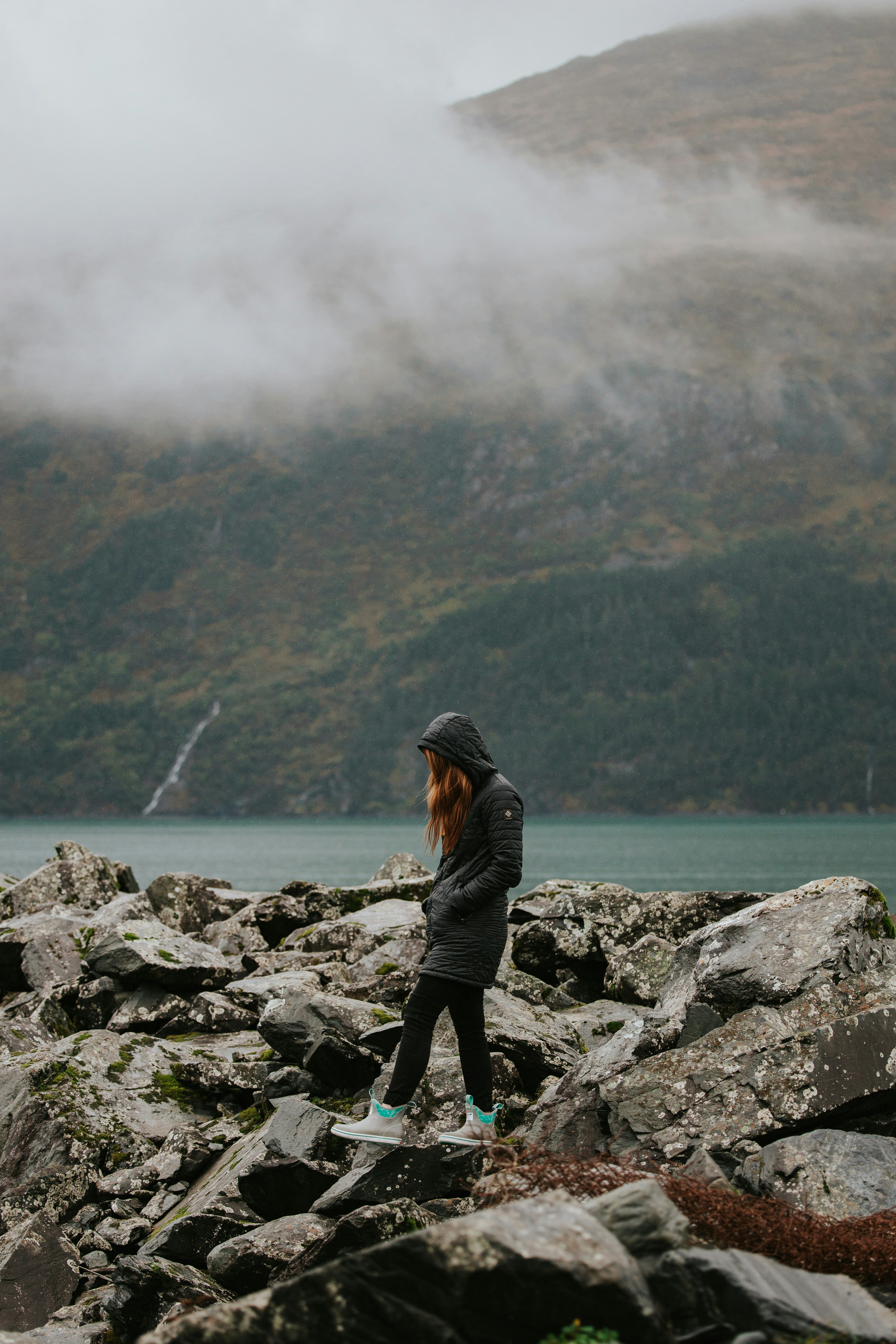 woman in black jacket and black pants standing on rocky shore during daytime