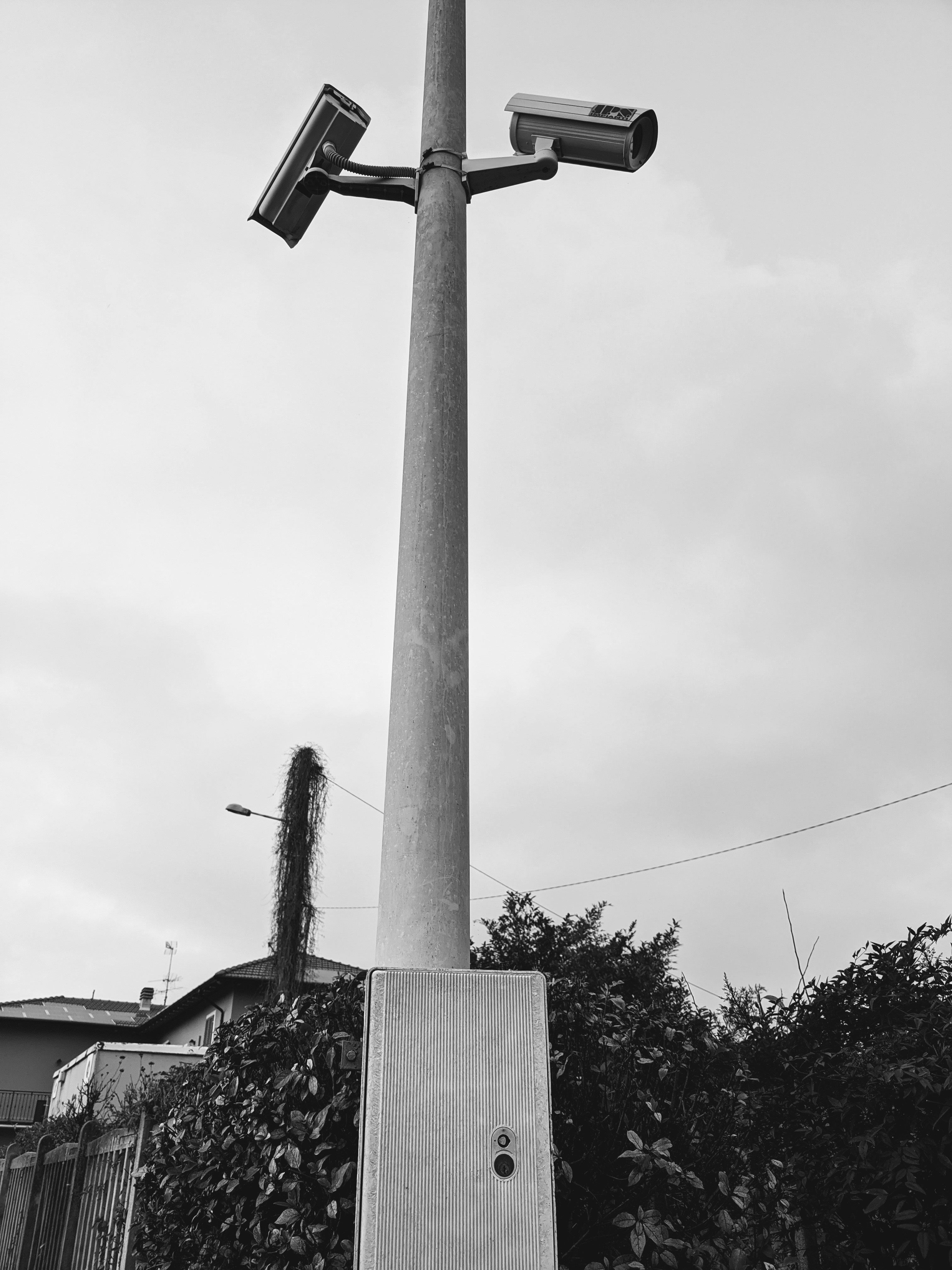 Surveillance cameras mounted on a tall pole against a cloudy sky, emphasizing urban security measures.