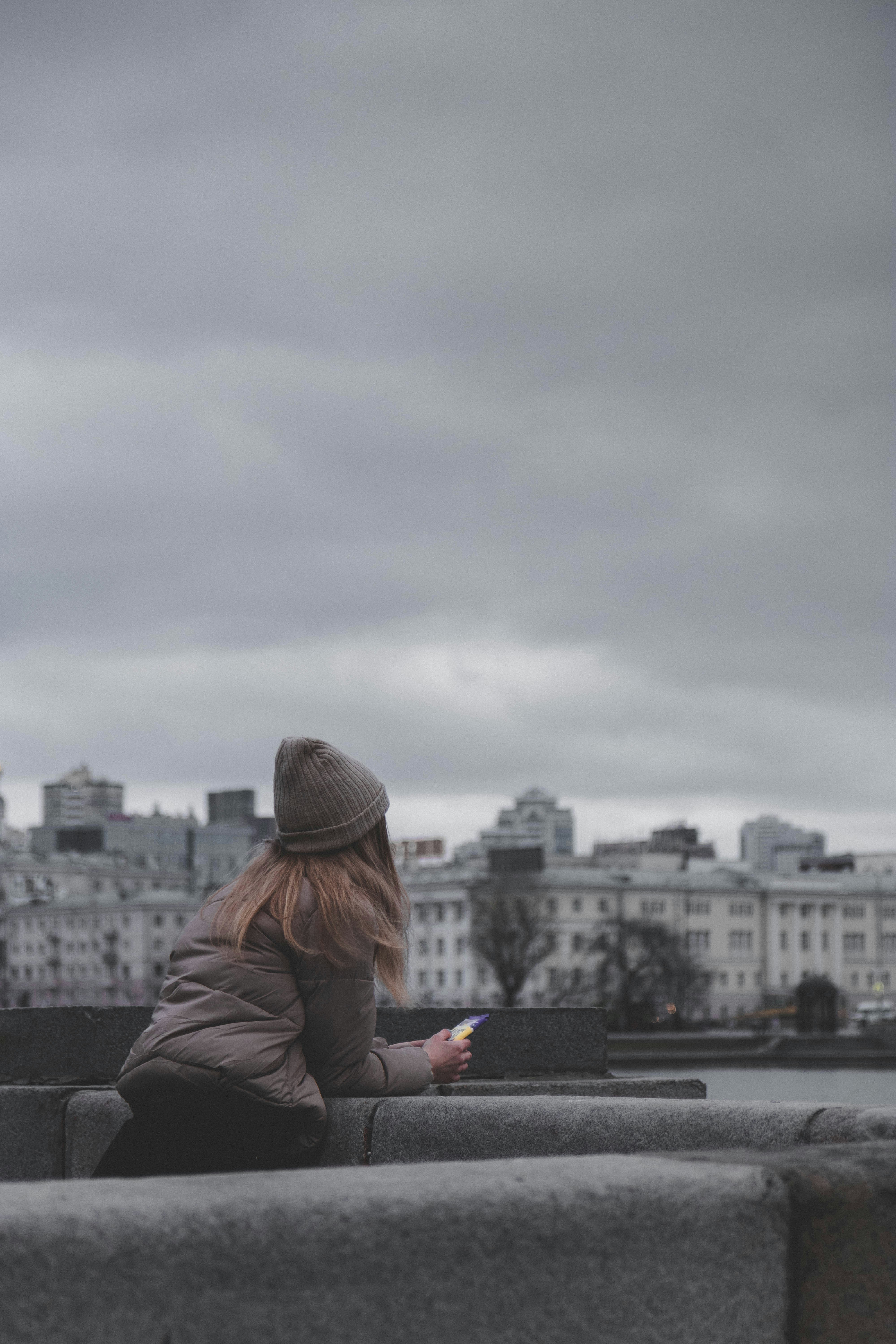 Woman in brown jacket sitting on the edge of a building photo – Free ...