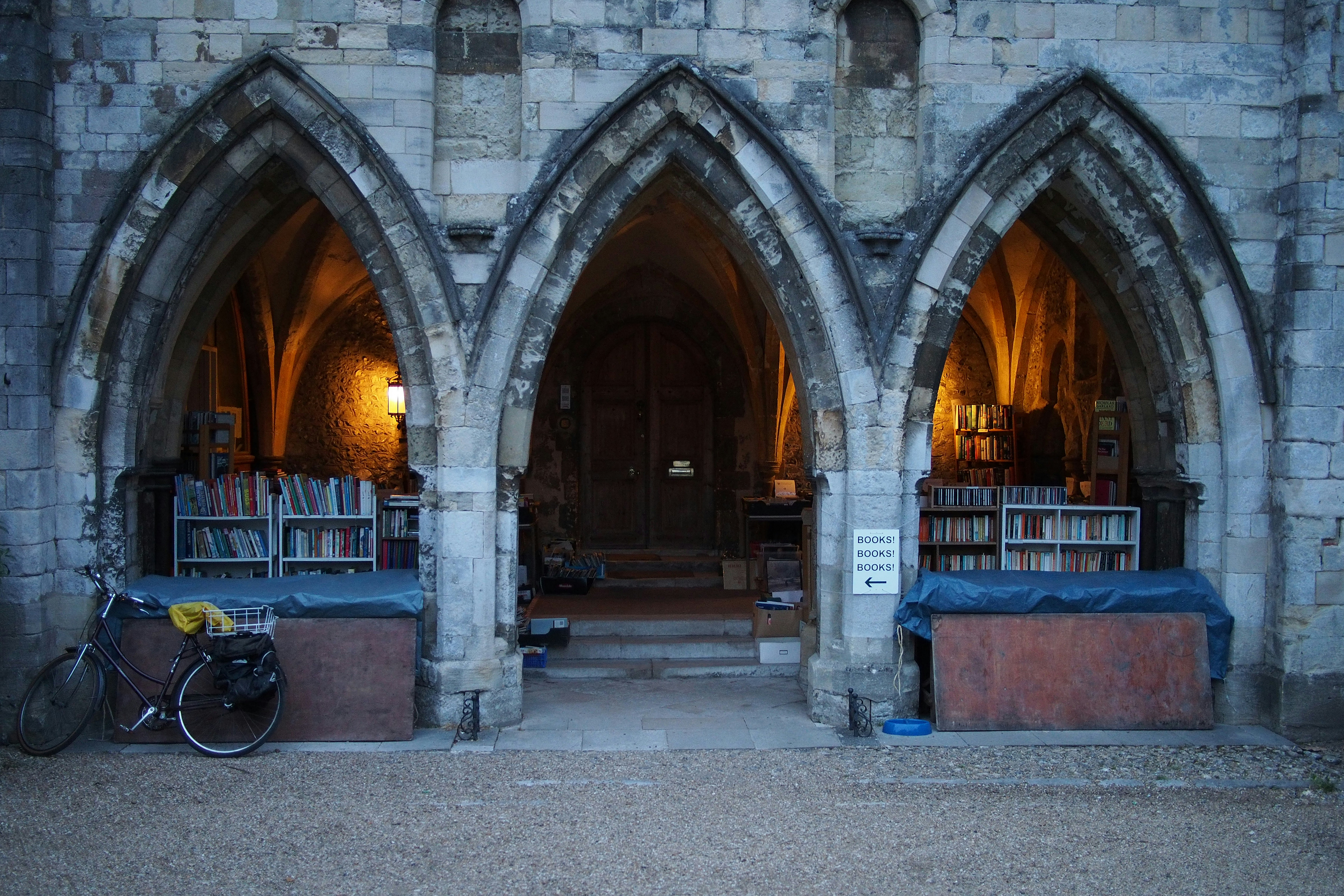 Gothic arches shelter a library entrance with warm lighting and a parked bicycle.