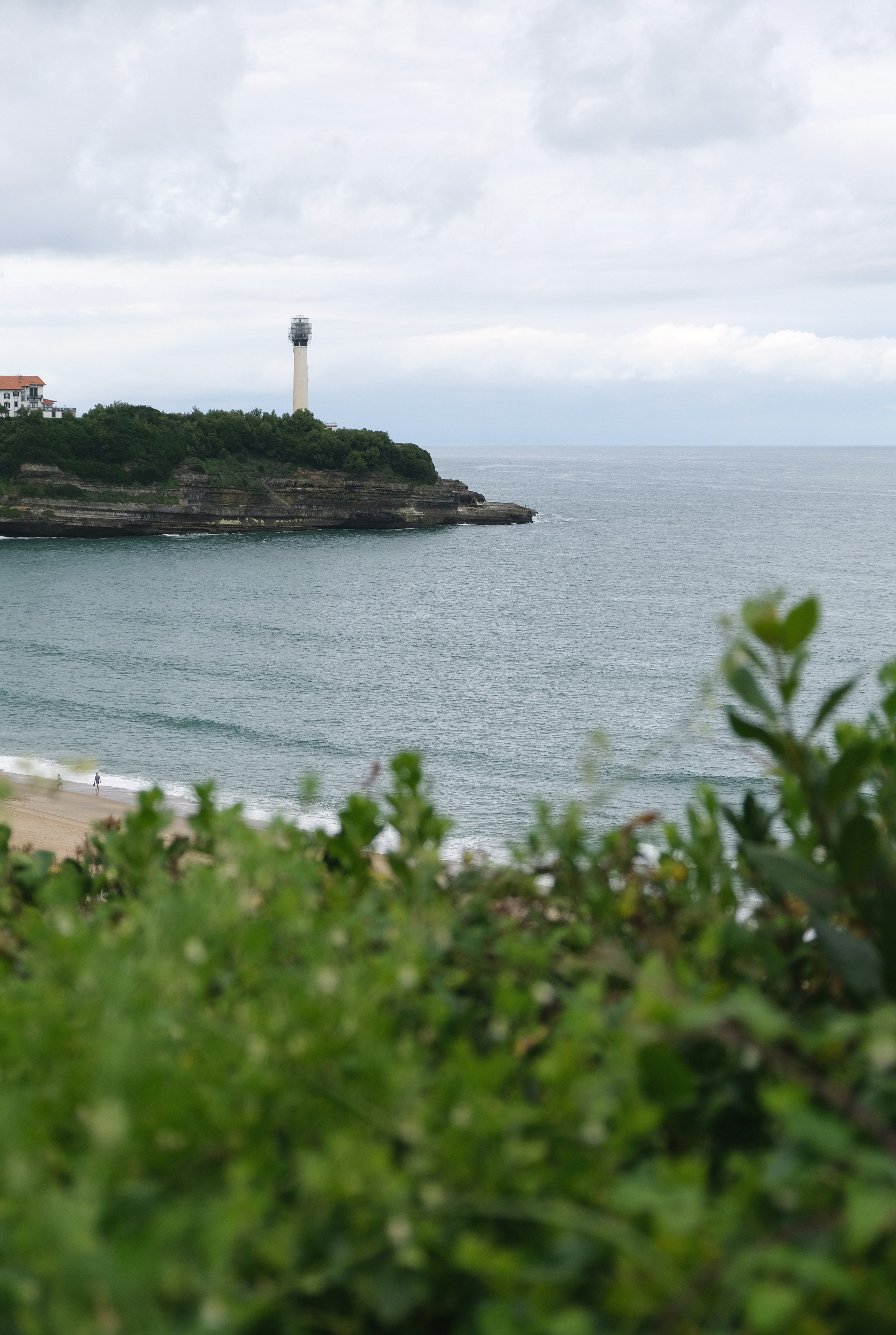 A lighthouse stands sentinel over a tranquil beach, framed by lush greenery and gentle waves. The scene captures the harmony of land and sea.