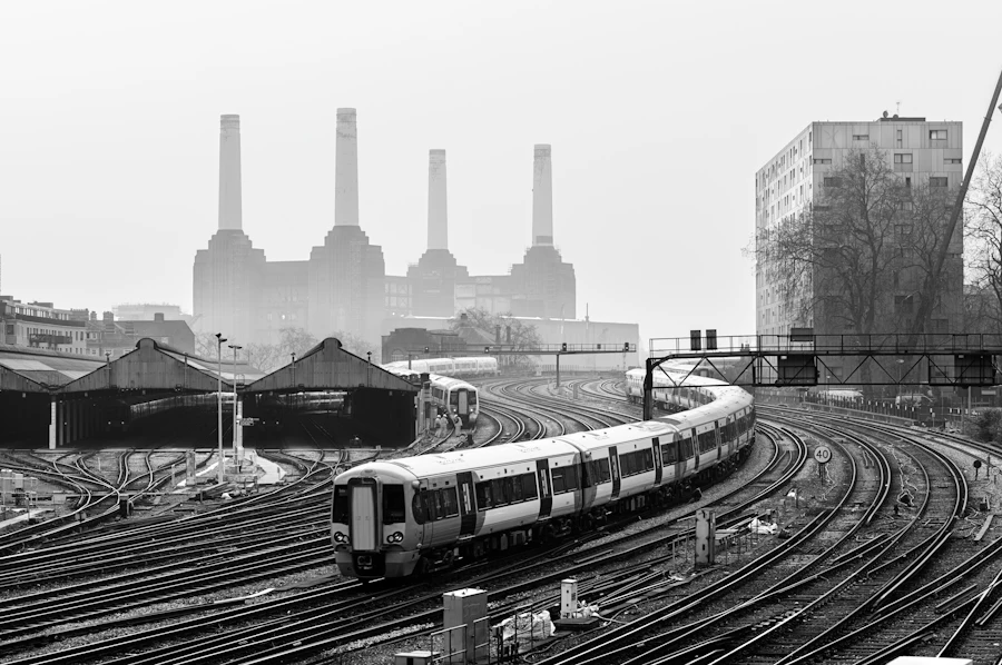 A sleek train winds through an industrial landscape, framed by iconic smokestacks and a foggy atmosphere. The monochrome palette enhances the contrast between the train and its surroundings.