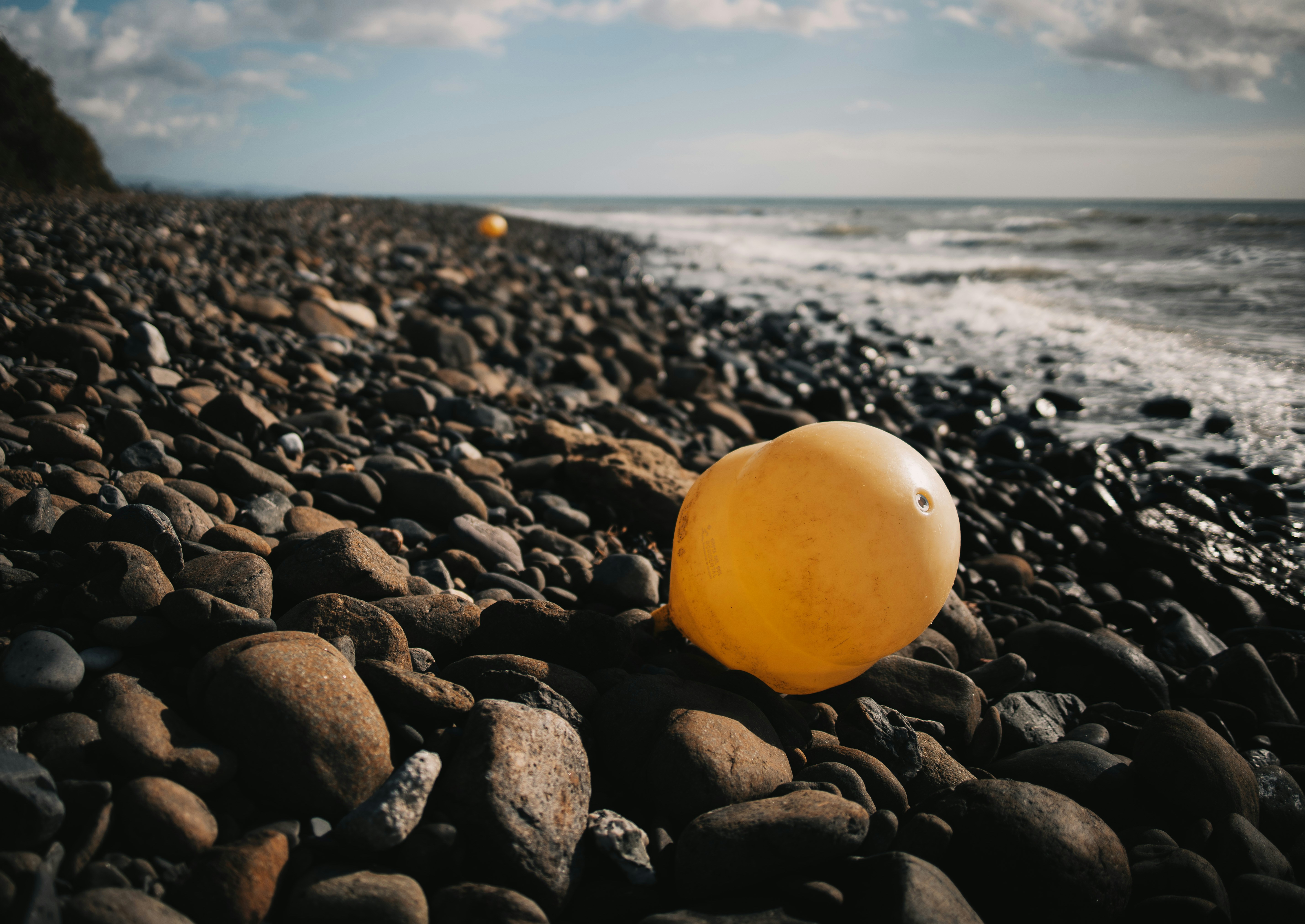 Lone Yellow Buoy Resting Among Pebbles on a Windwashed Shore