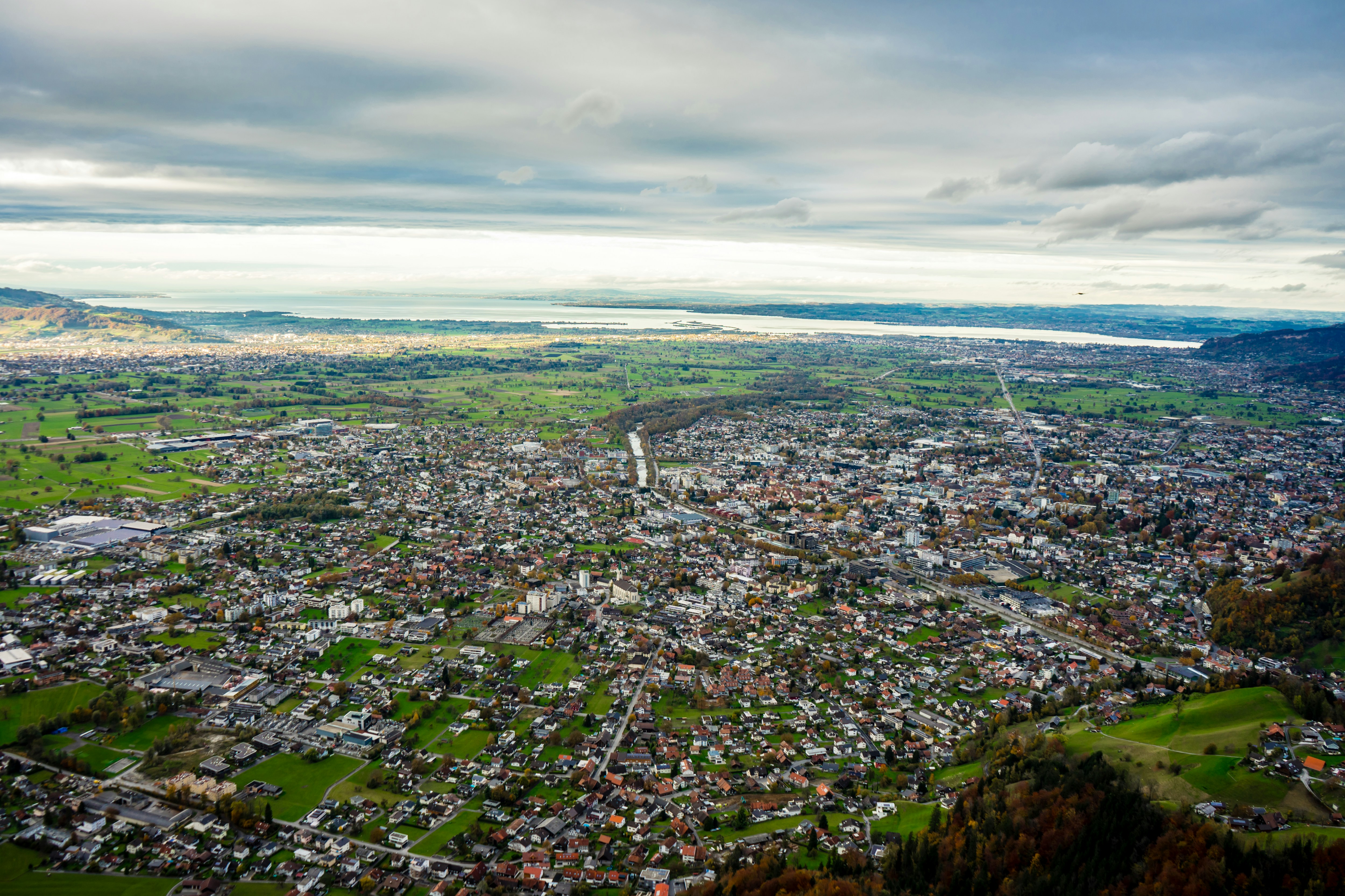 Aerial view of a city sprawling across lush green fields under a cloudy sky.