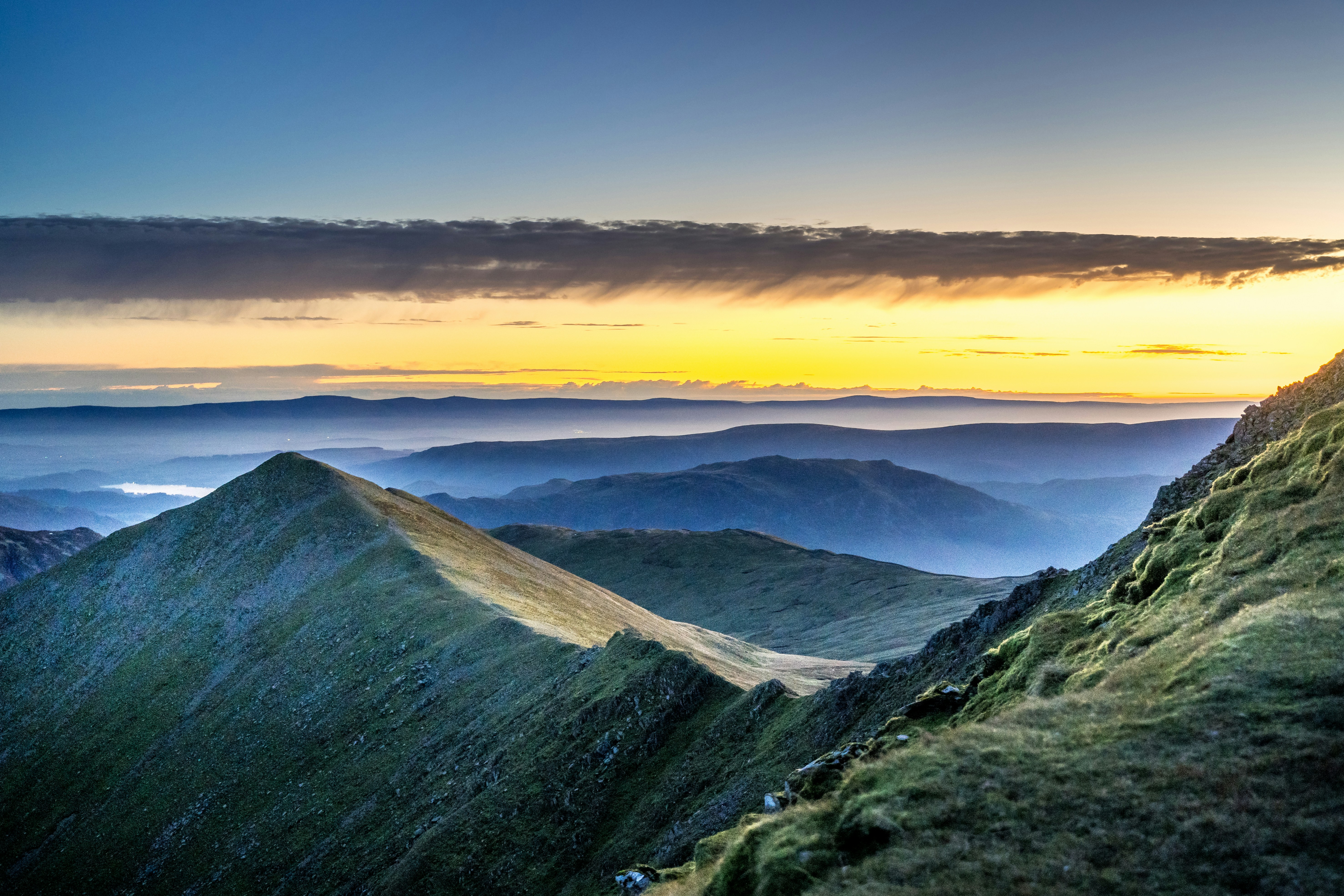 Golden light spills over undulating hills, casting shadows and highlighting the textured landscape at twilight.