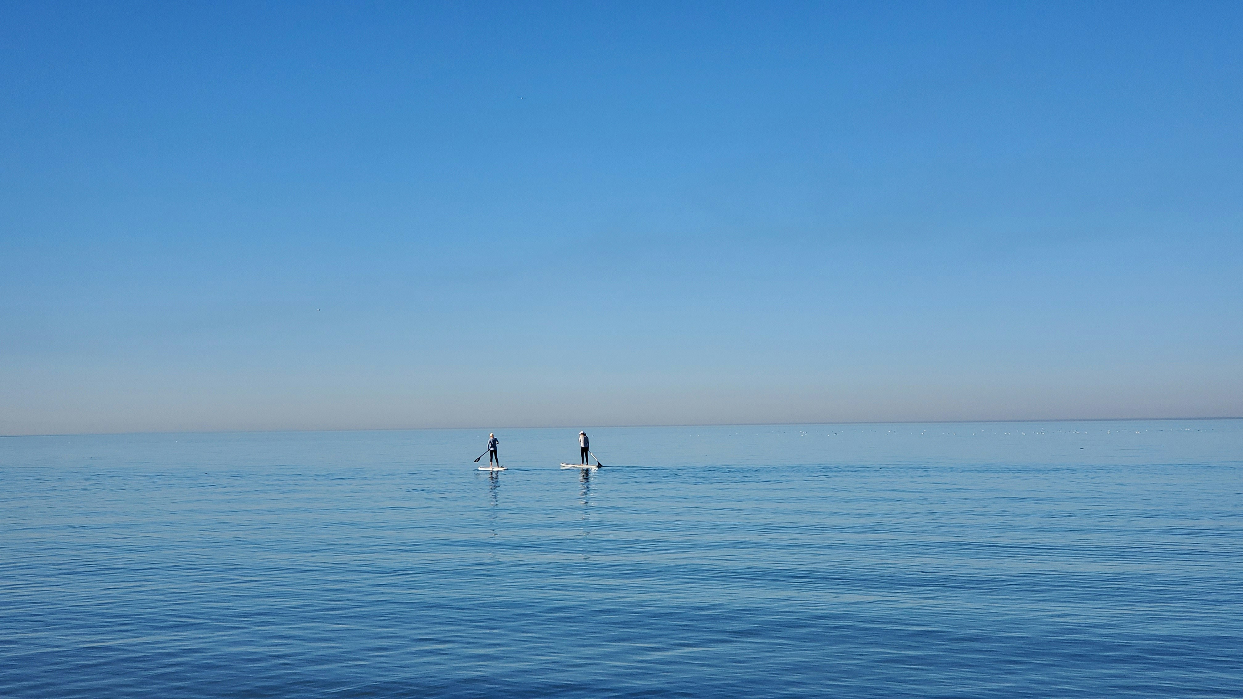 Two sailboats on a calm blue sea beneath a clear sky.