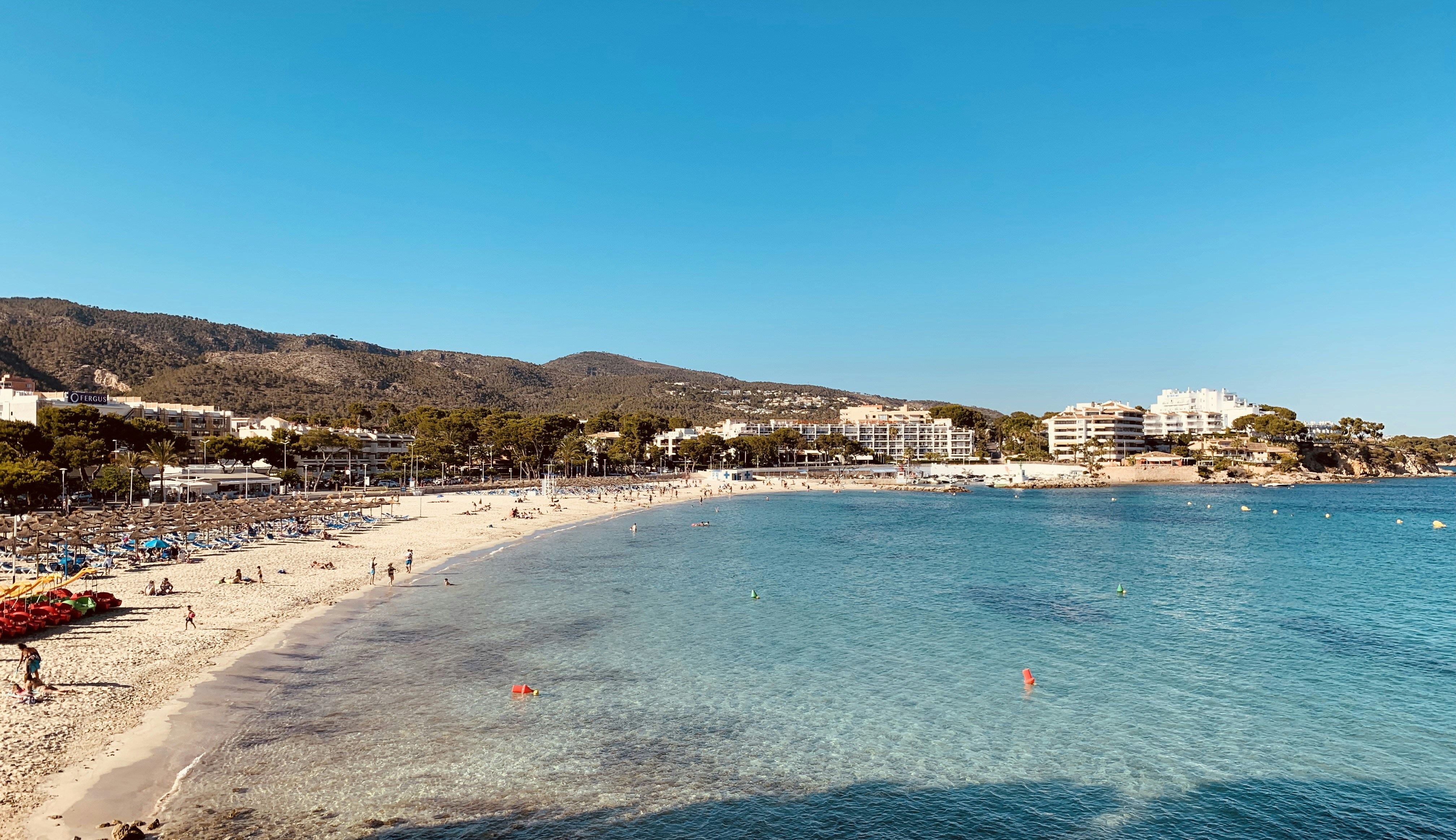 Tranquil beach with clear blue waters and distant mountains under a bright sky.