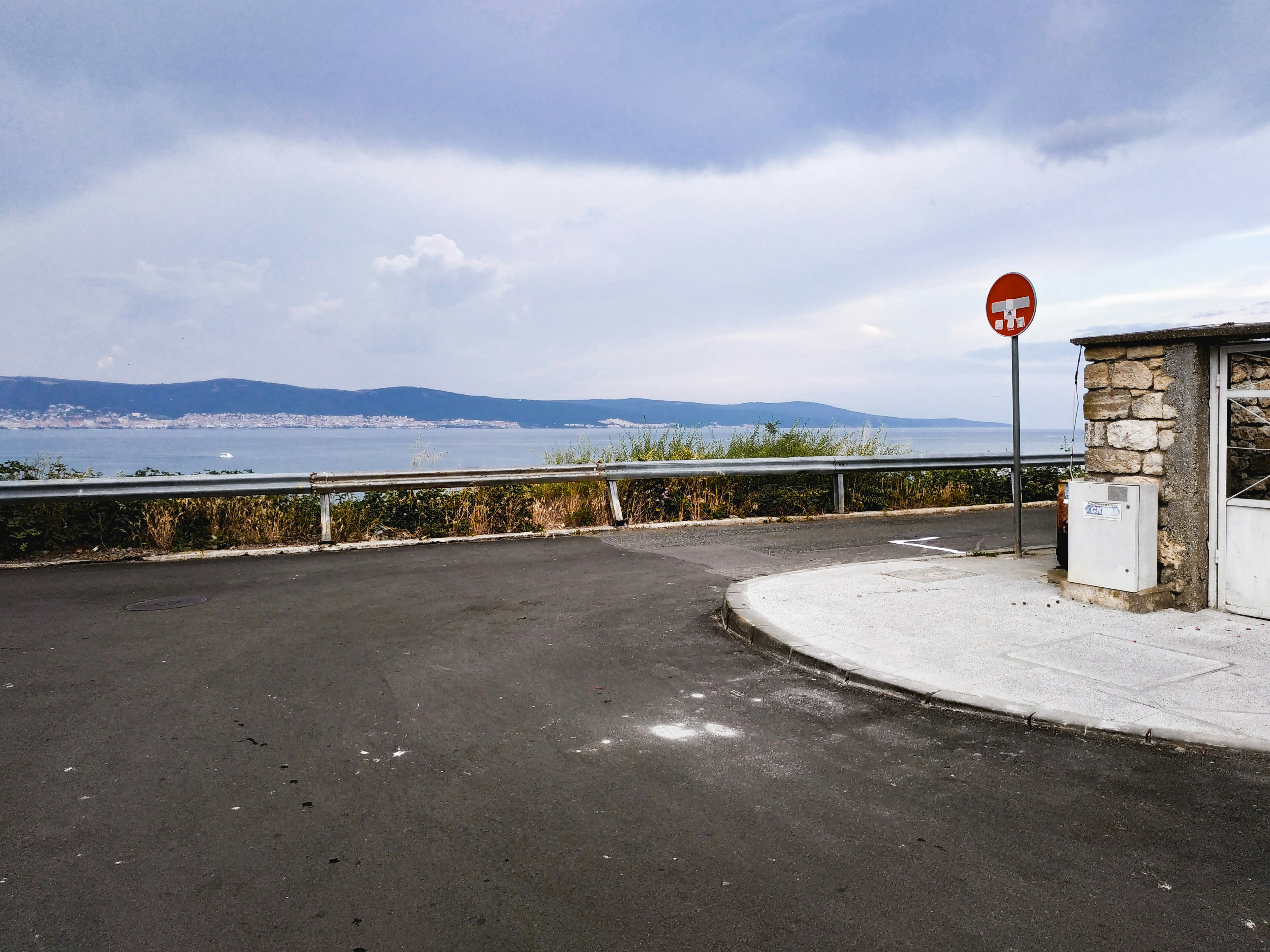 Red Sign at the Cliffside Curve: A Quiet Seascape Under Grey Skies