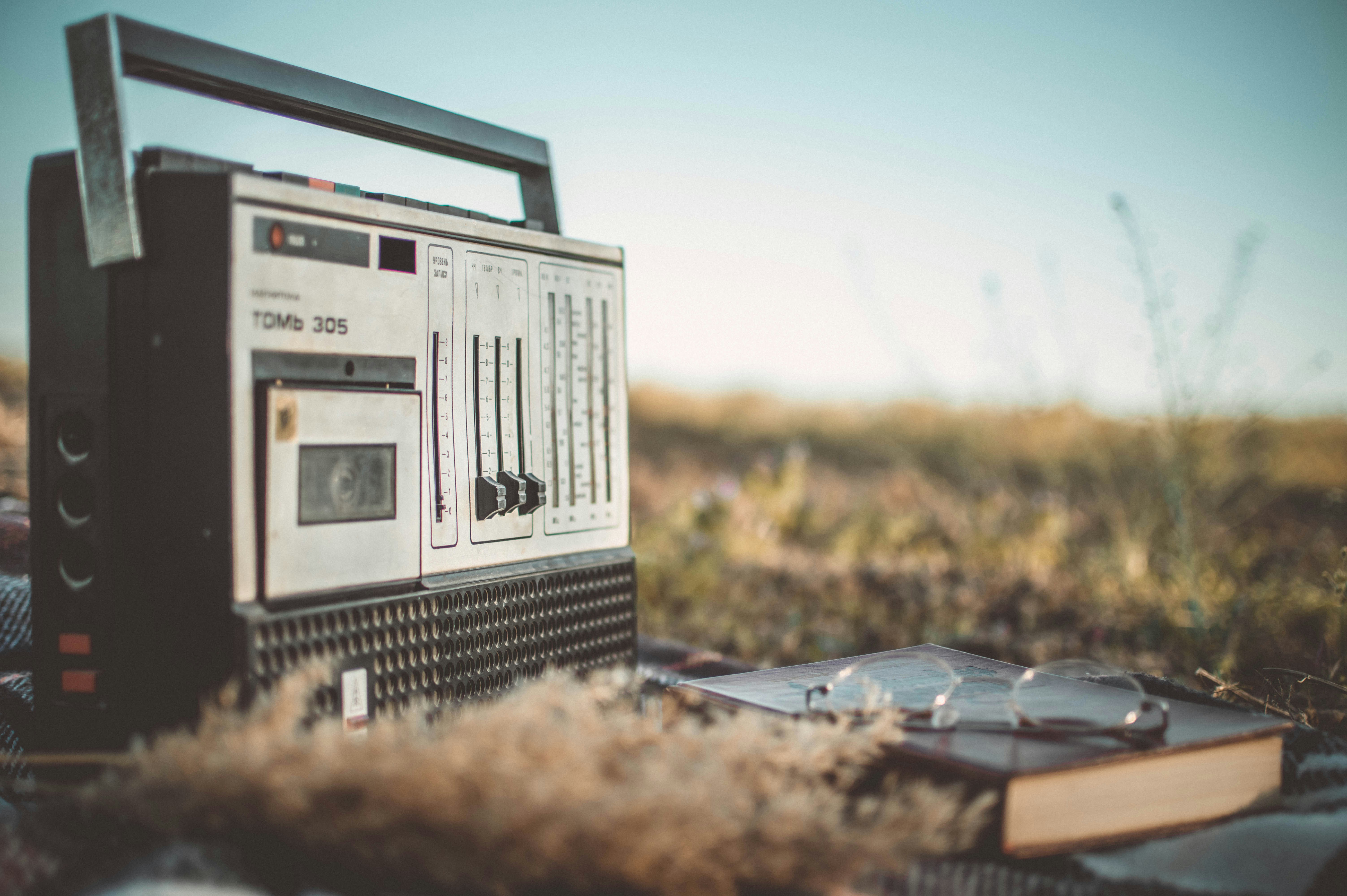 Sunlit Relic: A Vintage Radio Paired with a Book and Glasses in a Quiet Field