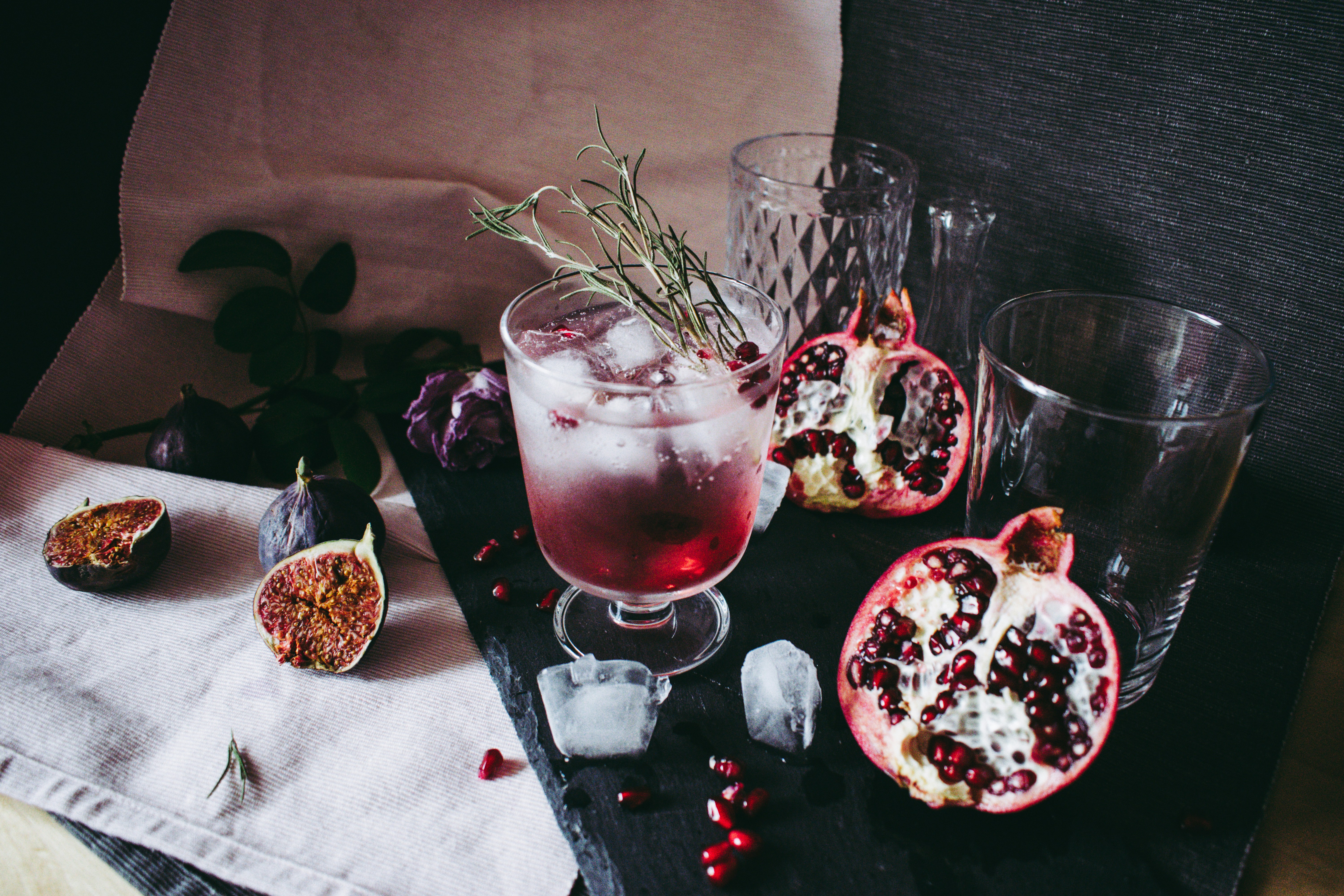 Crimson Cocktail, Rosemary Sprig, and Pomegranate Halos on a Velvet Table